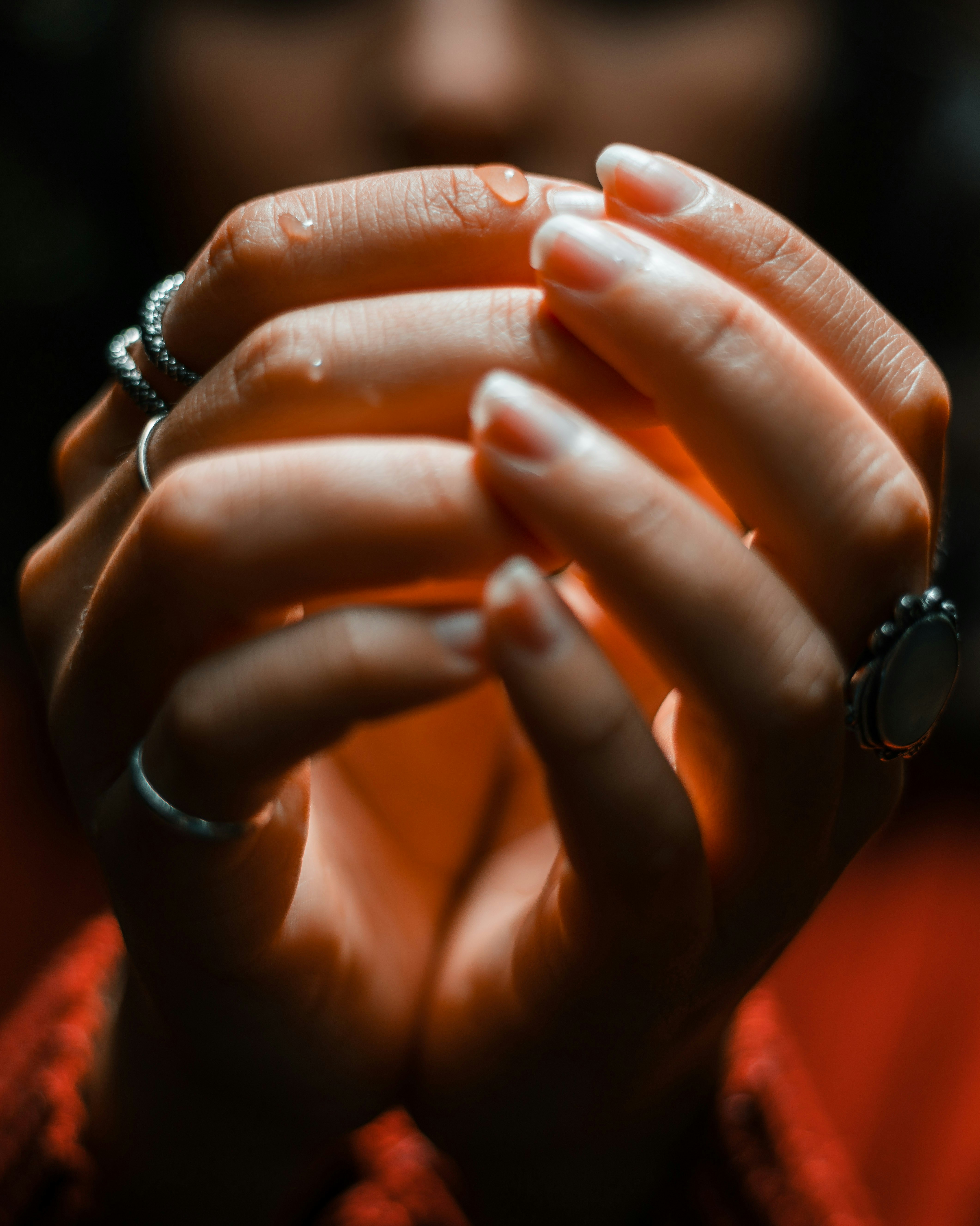 Delicate hands adorned with rings gently cradle droplets of water, emphasizing texture and intimacy in a soft-focus background.
