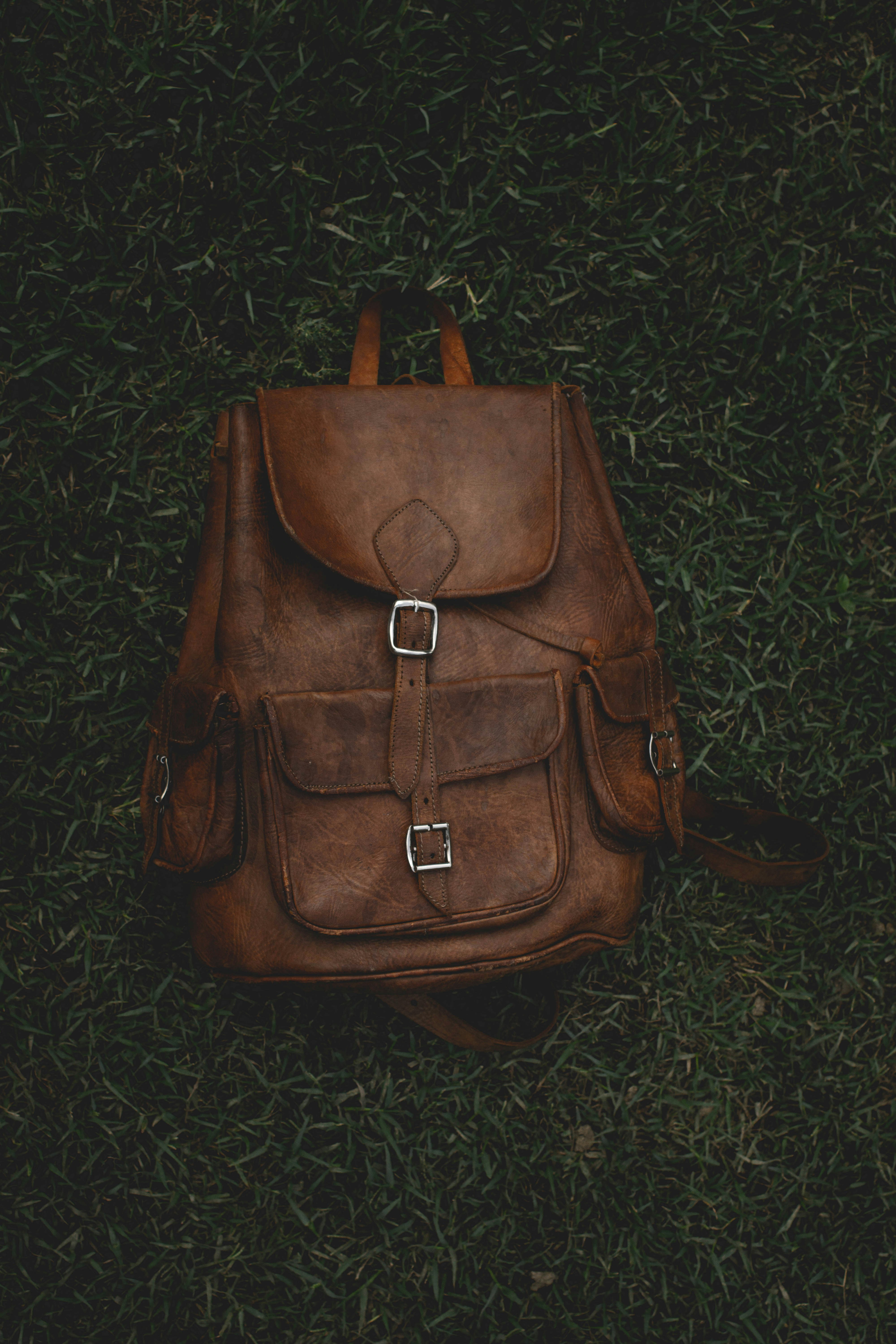 Vintage leather backpack resting on lush green grass, showcasing its rich texture and craftsmanship.