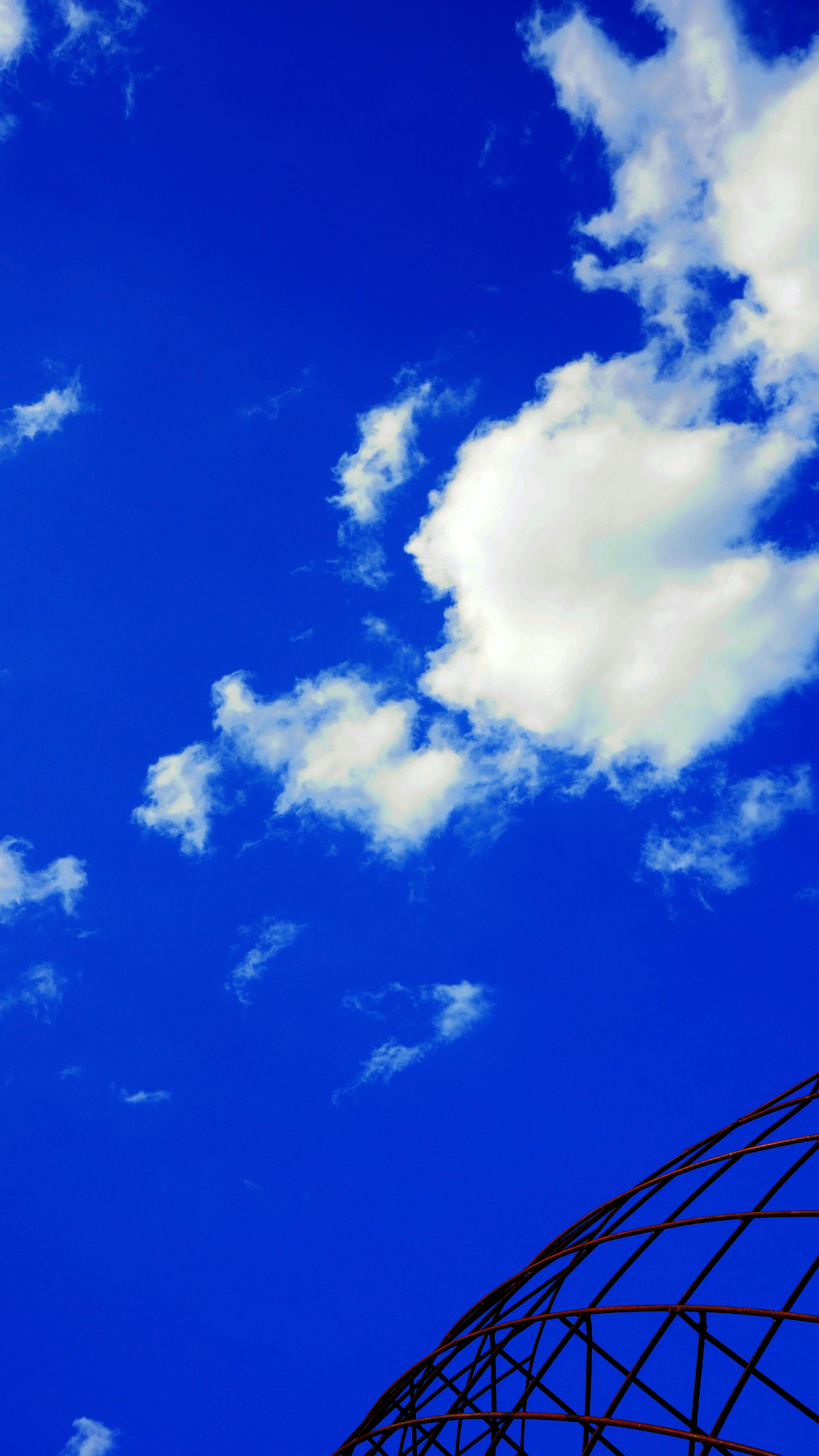A striking view of a blue sky adorned with fluffy clouds, contrasted by the geometric lines of a metal structure below.
