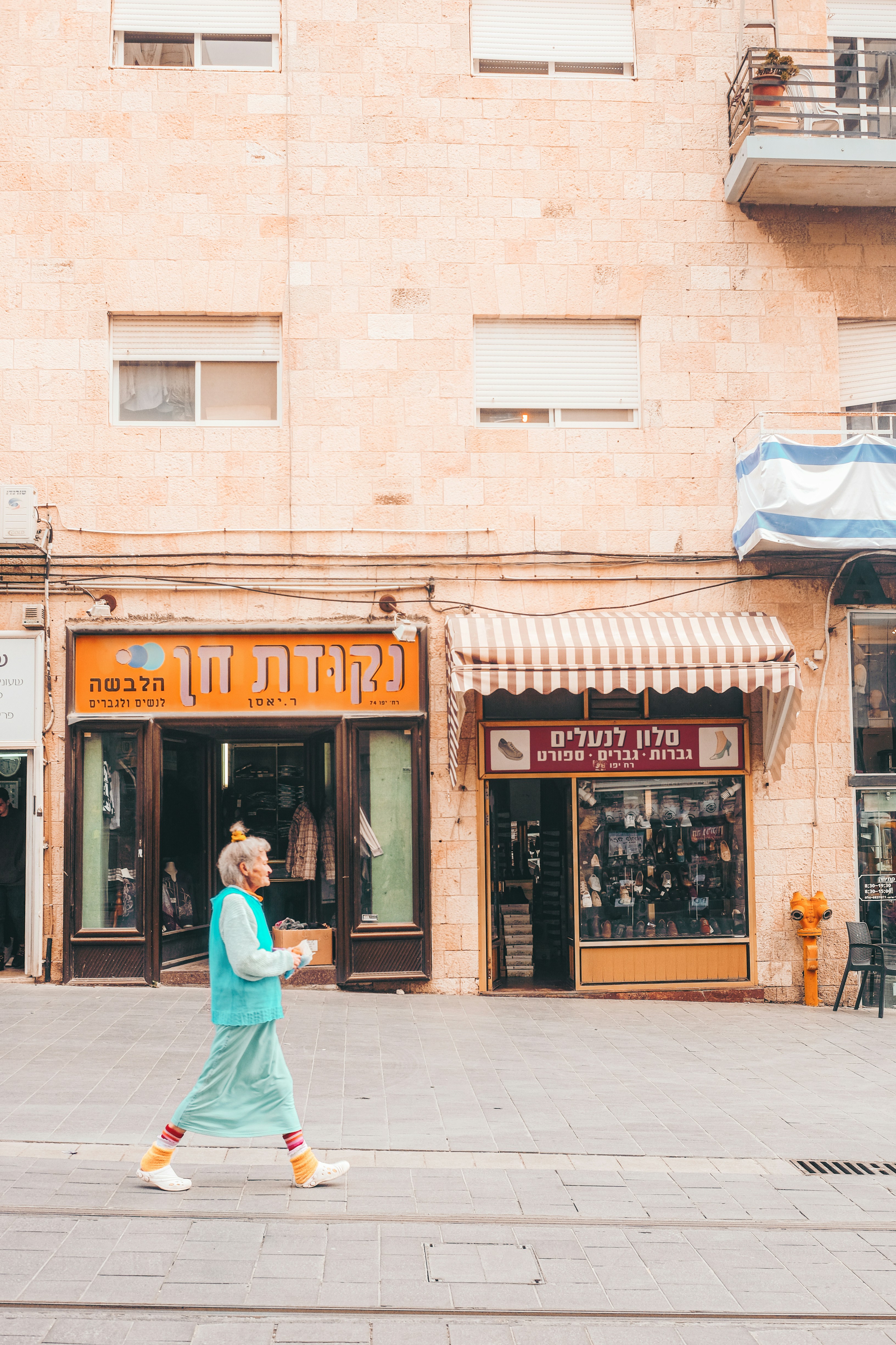  strolling elder in front of warm-toned shops under striped awning