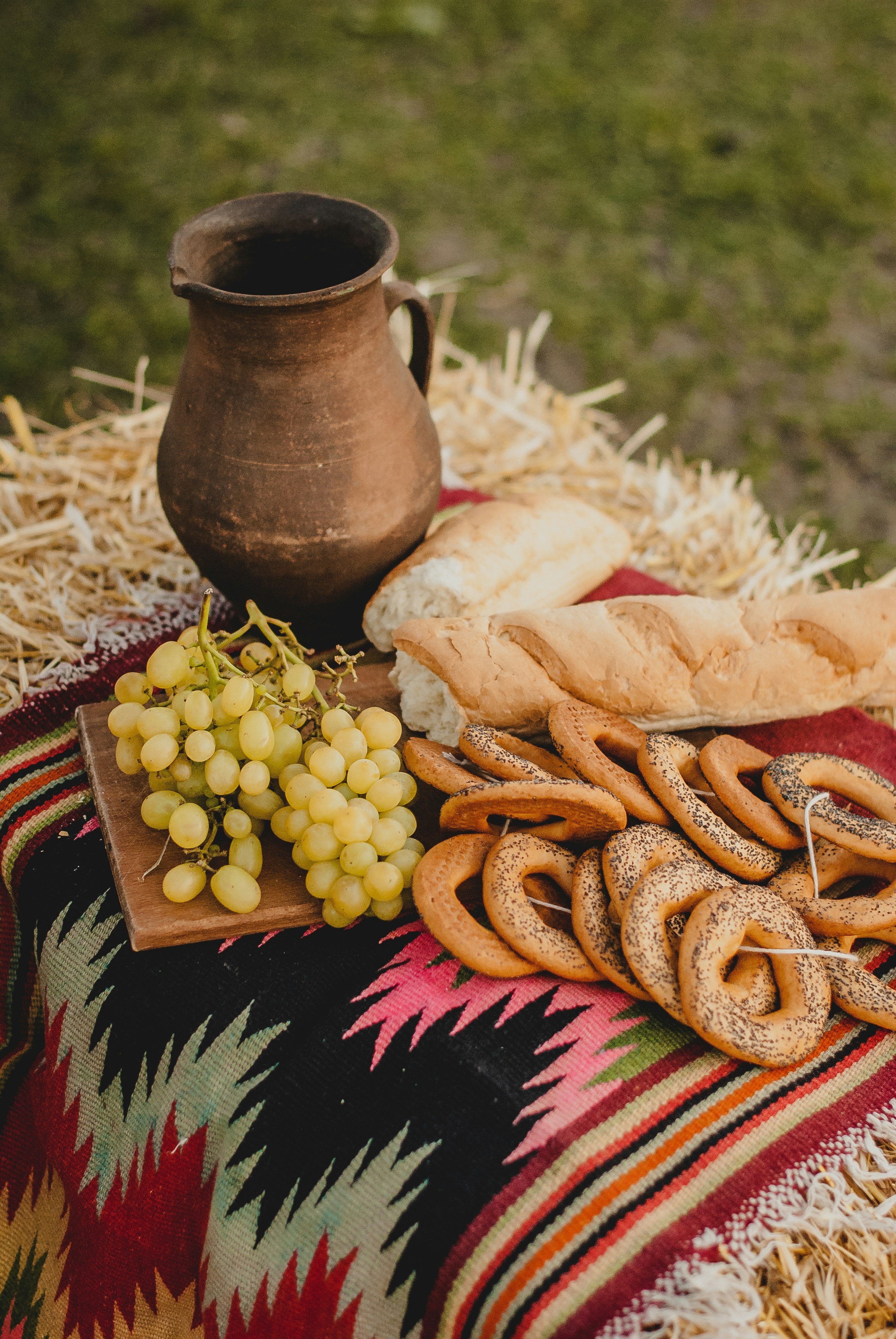 A rustic display of fresh grapes, bread, and traditional pastries arranged on a vibrant woven textile. The earthy pottery jug adds to the warm, inviting atmosphere.