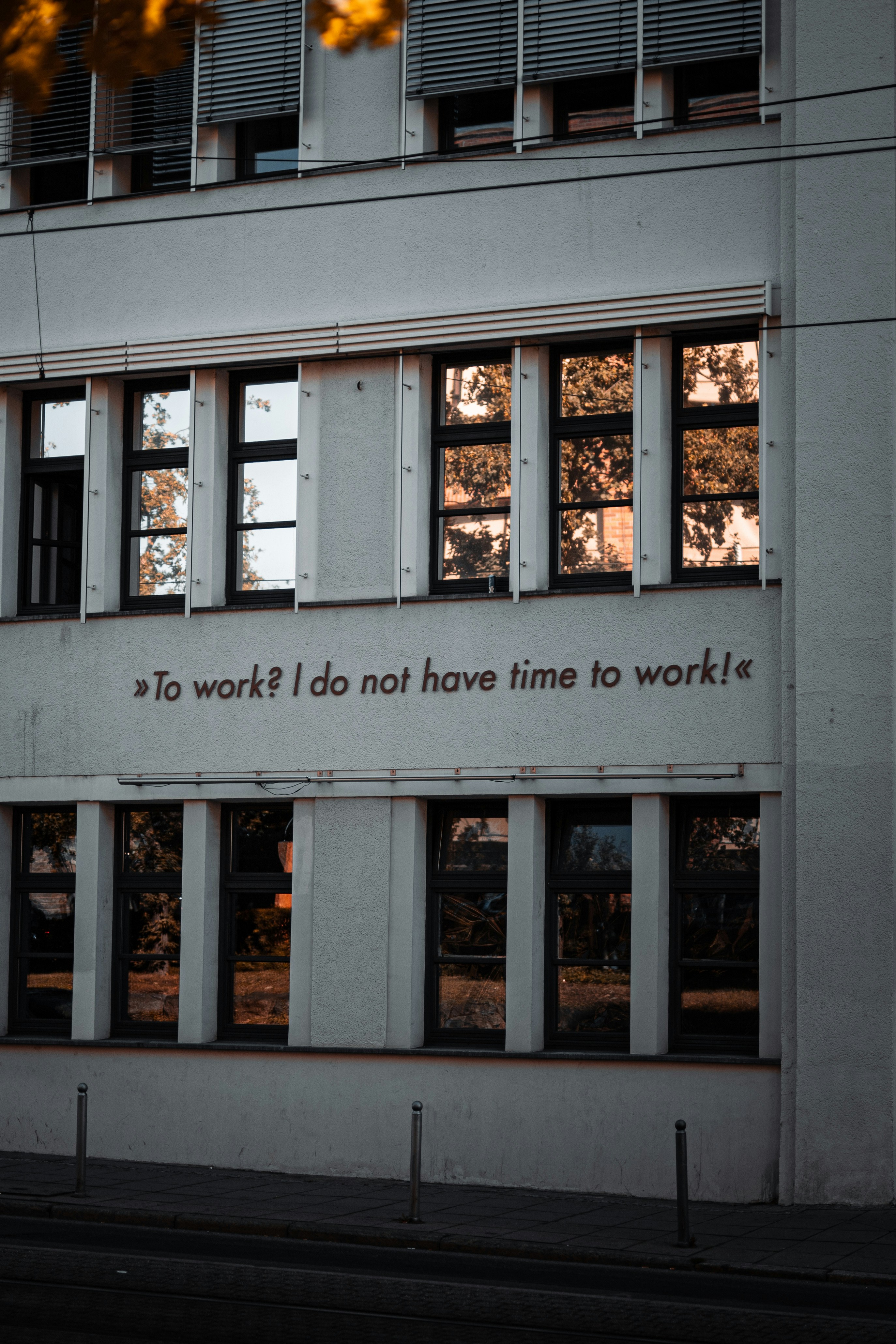 Quote on a building facade reflecting modern work-life sentiments, surrounded by window reflections and urban architecture.