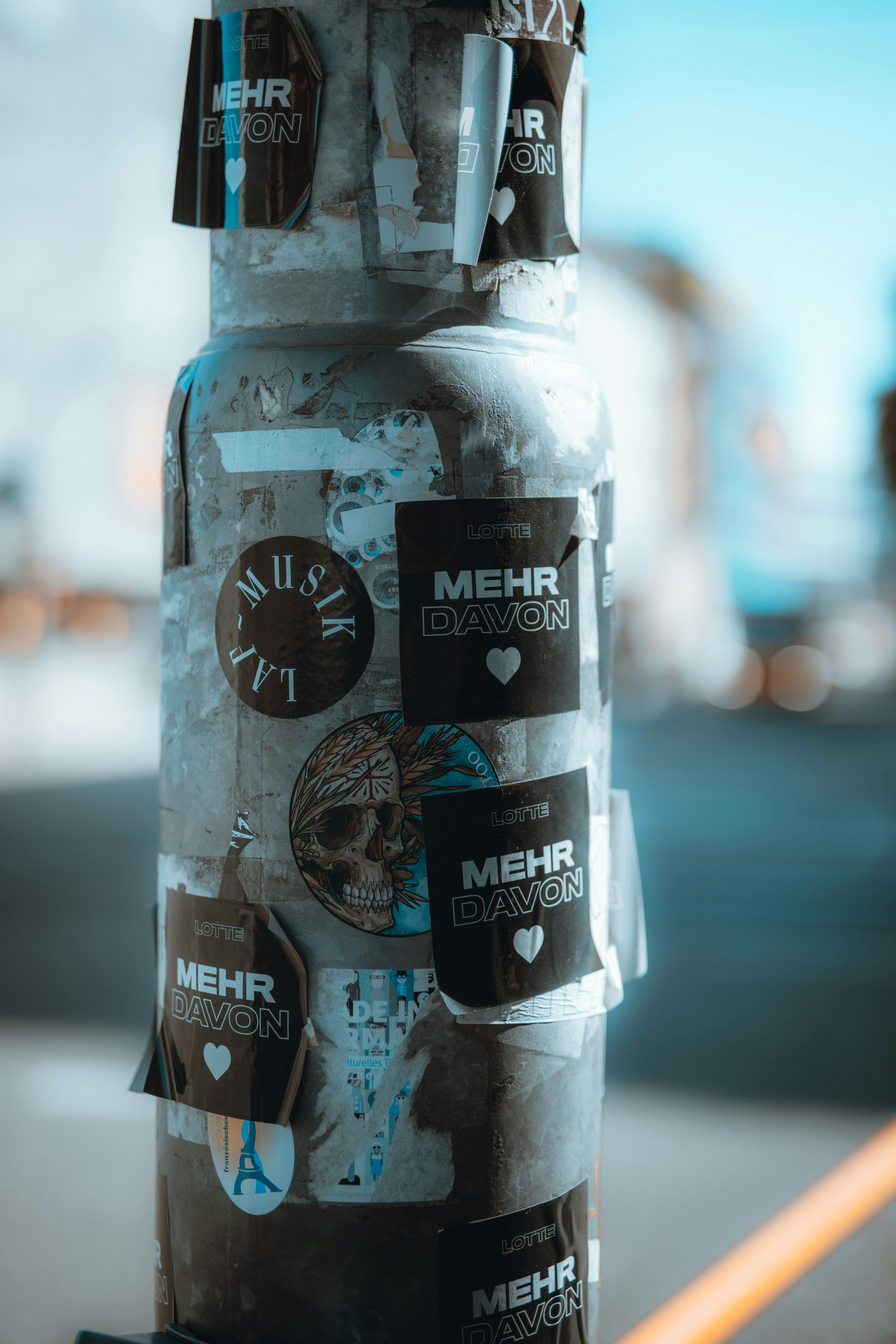 A close-up of a weathered pole adorned with various stickers, showcasing urban art and messages. The vibrant colors contrast against the muted background.