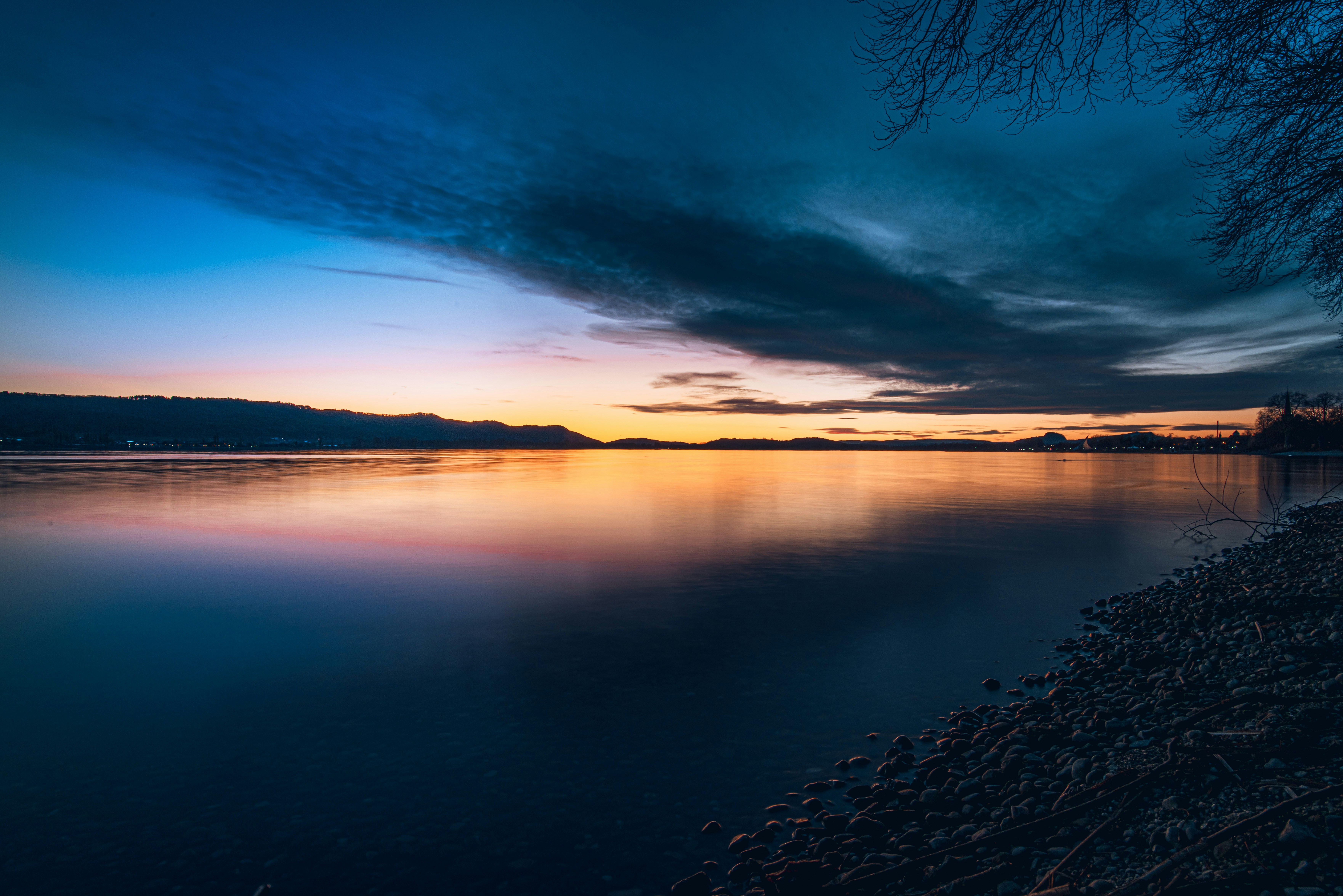 Serene lake reflecting vibrant hues of a sunset sky with silhouetted shoreline.