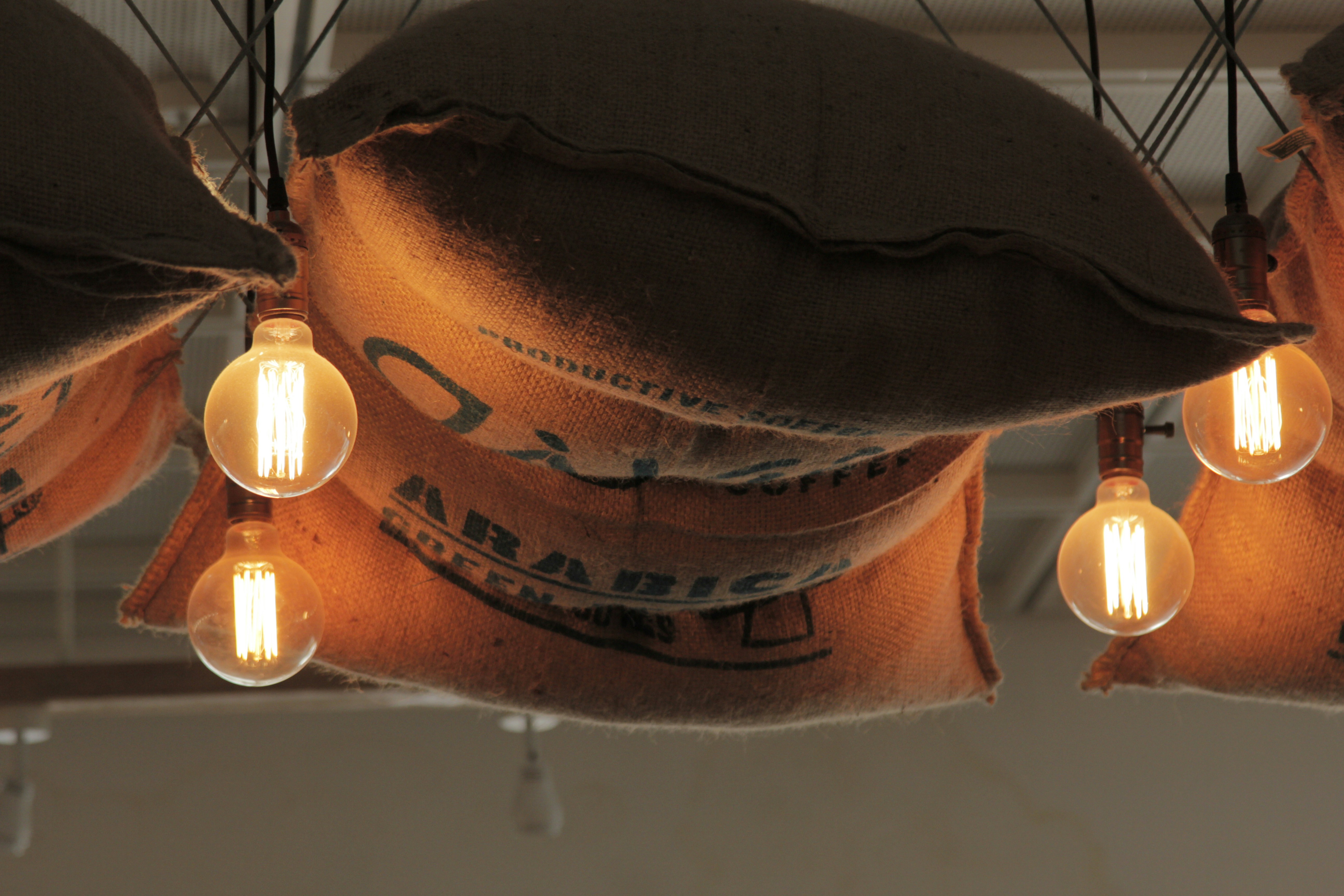 Hanging burlap sacks adorned with vintage light bulbs create a warm, inviting atmosphere in a cozy café setting.