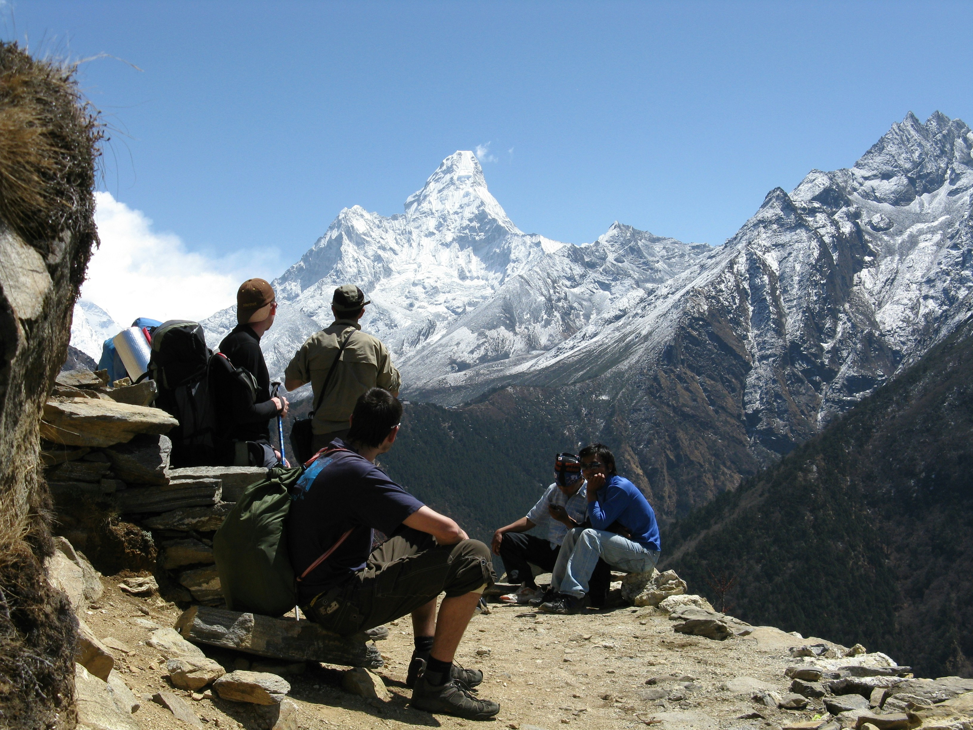 Hikers resting on a rocky ledge, surrounded by towering snow-capped peaks in the Himalayas.