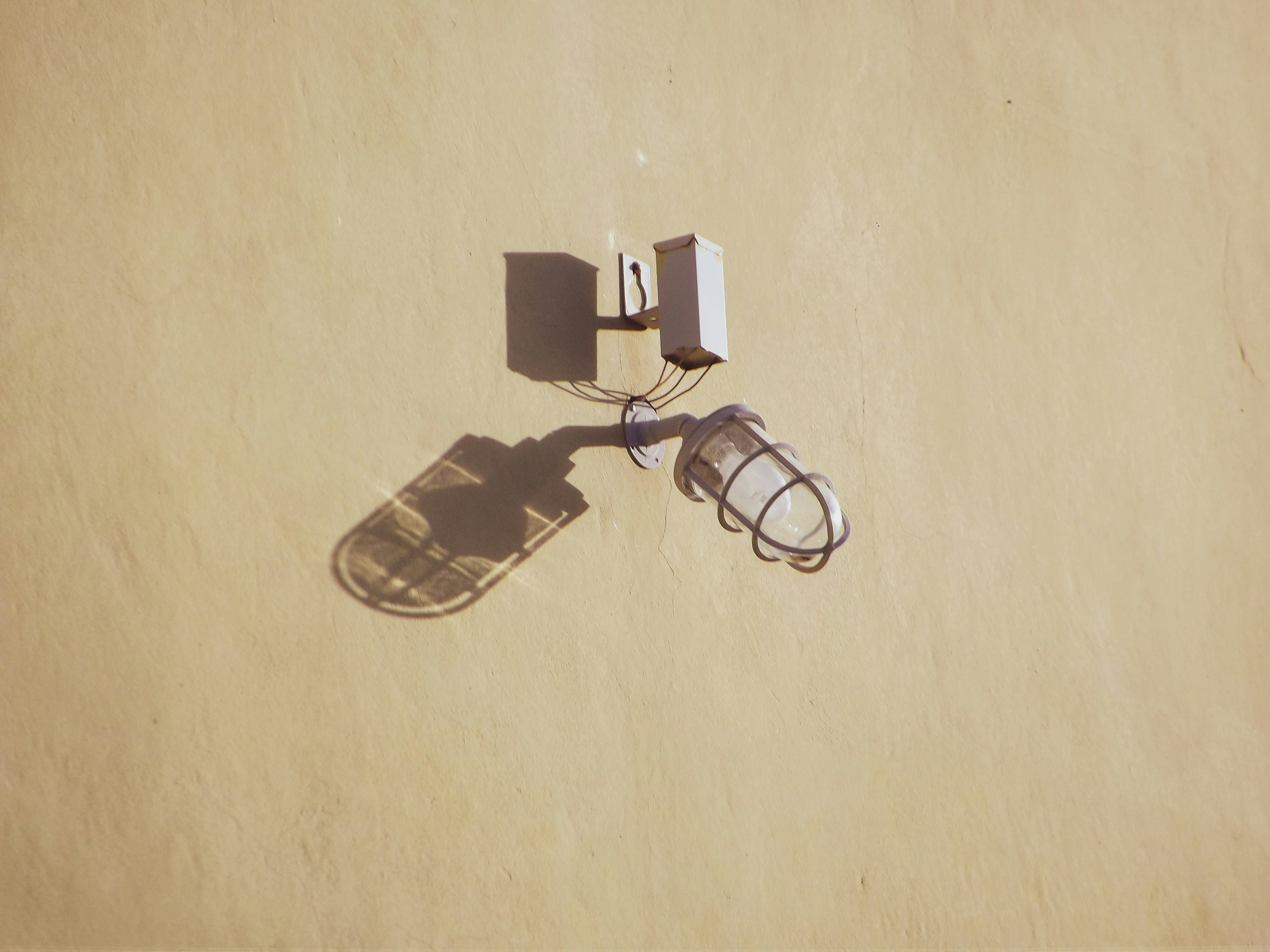 Caged Glow: A Minimalist Wall Sconce and Its Shadow