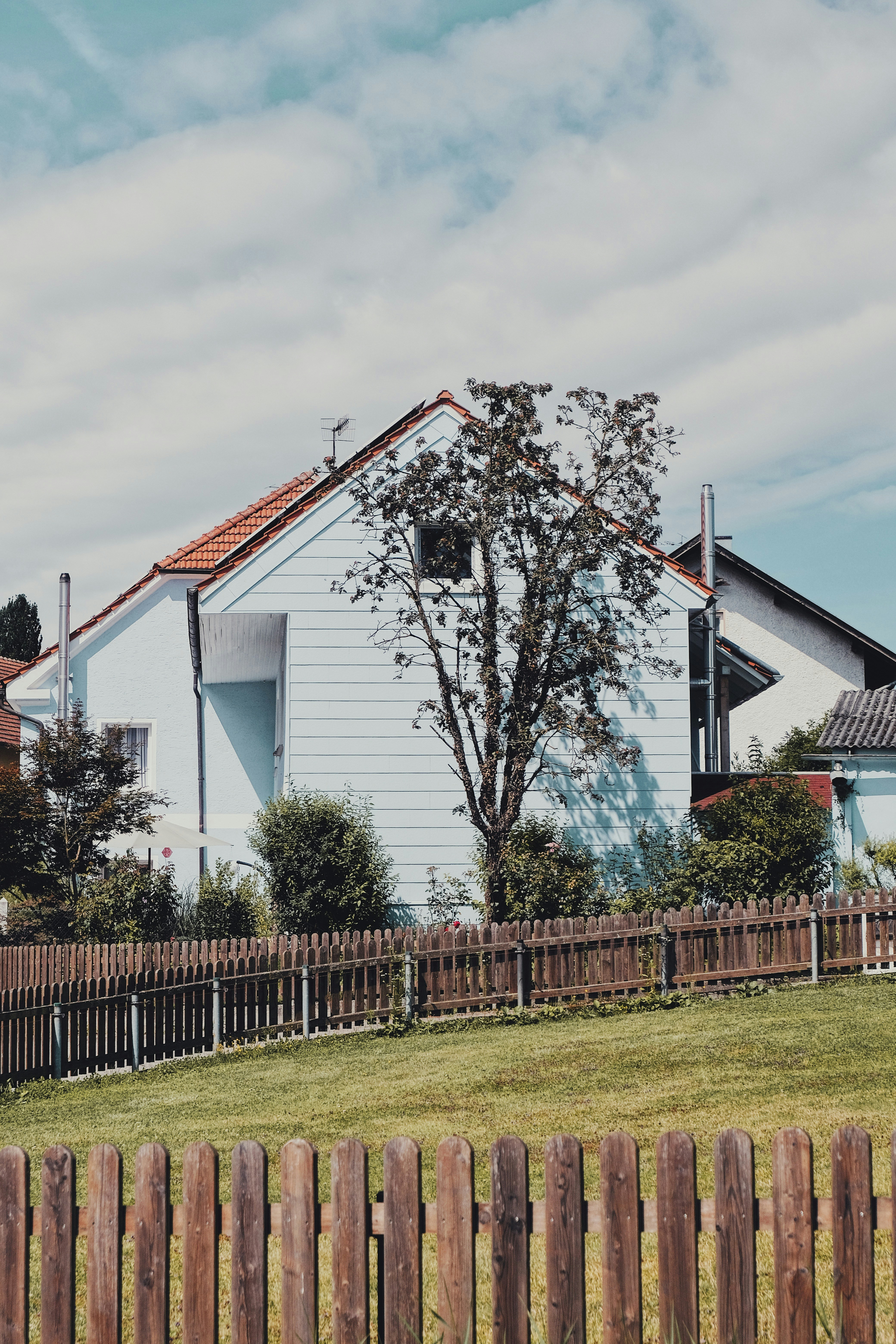 Blue House, Red Roof, and a Quiet Fence: A Suburban Portrait in Sunlit Pastels