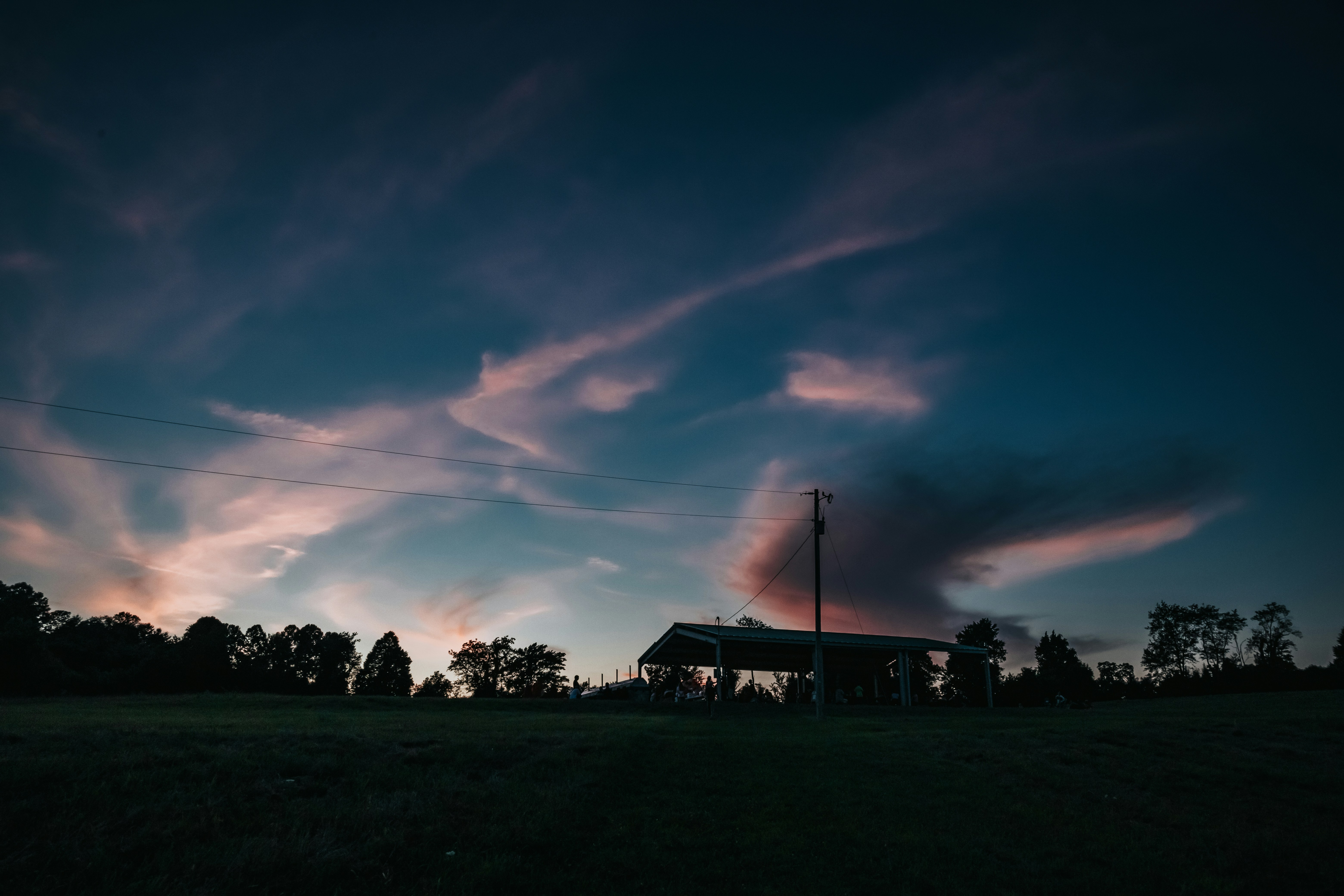 Silhouette of a rustic shelter against a vibrant twilight sky, with wispy clouds and a tranquil landscape. 