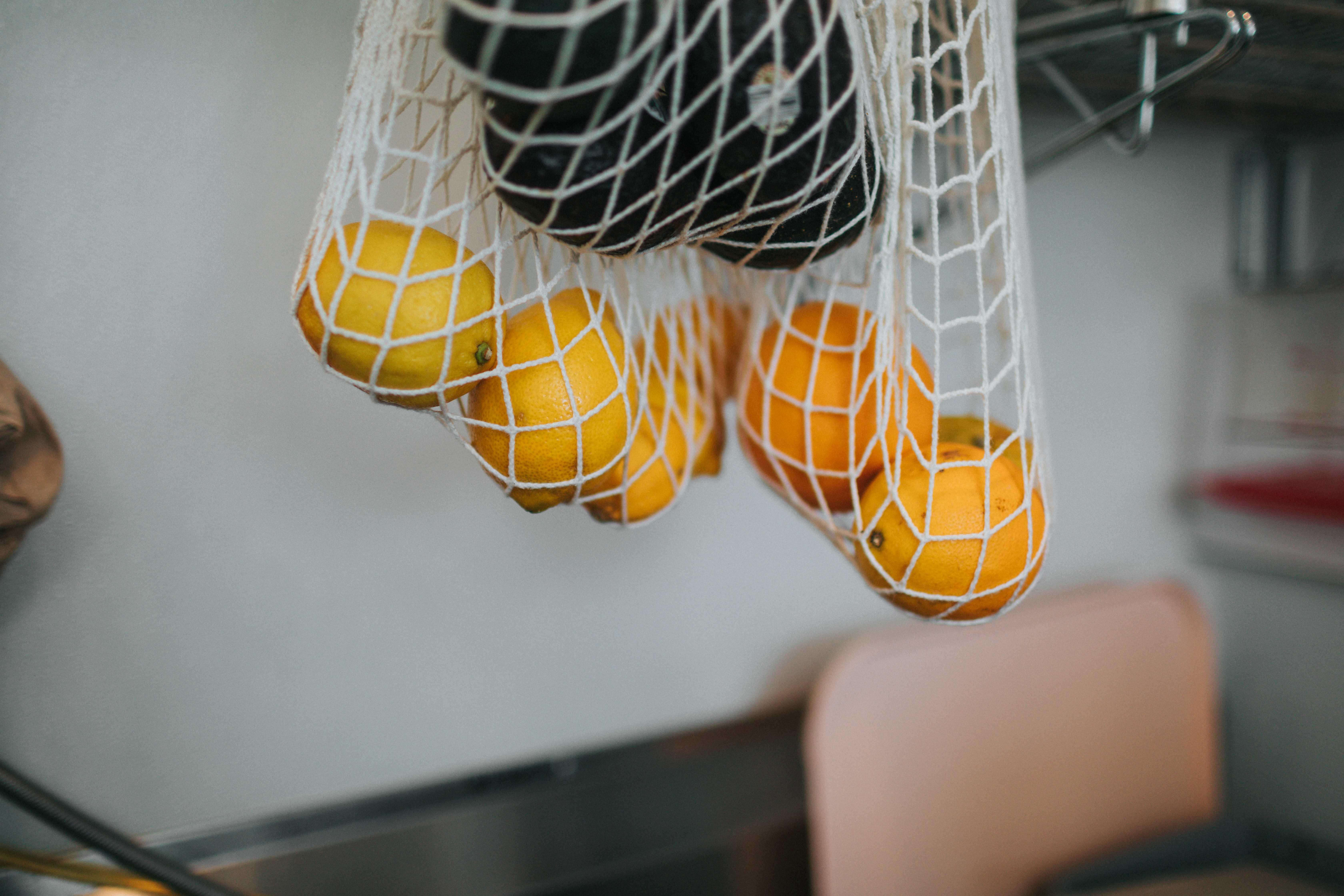 A mesh bag filled with vibrant oranges and a dark eggplant hangs in a stylish kitchen setting.