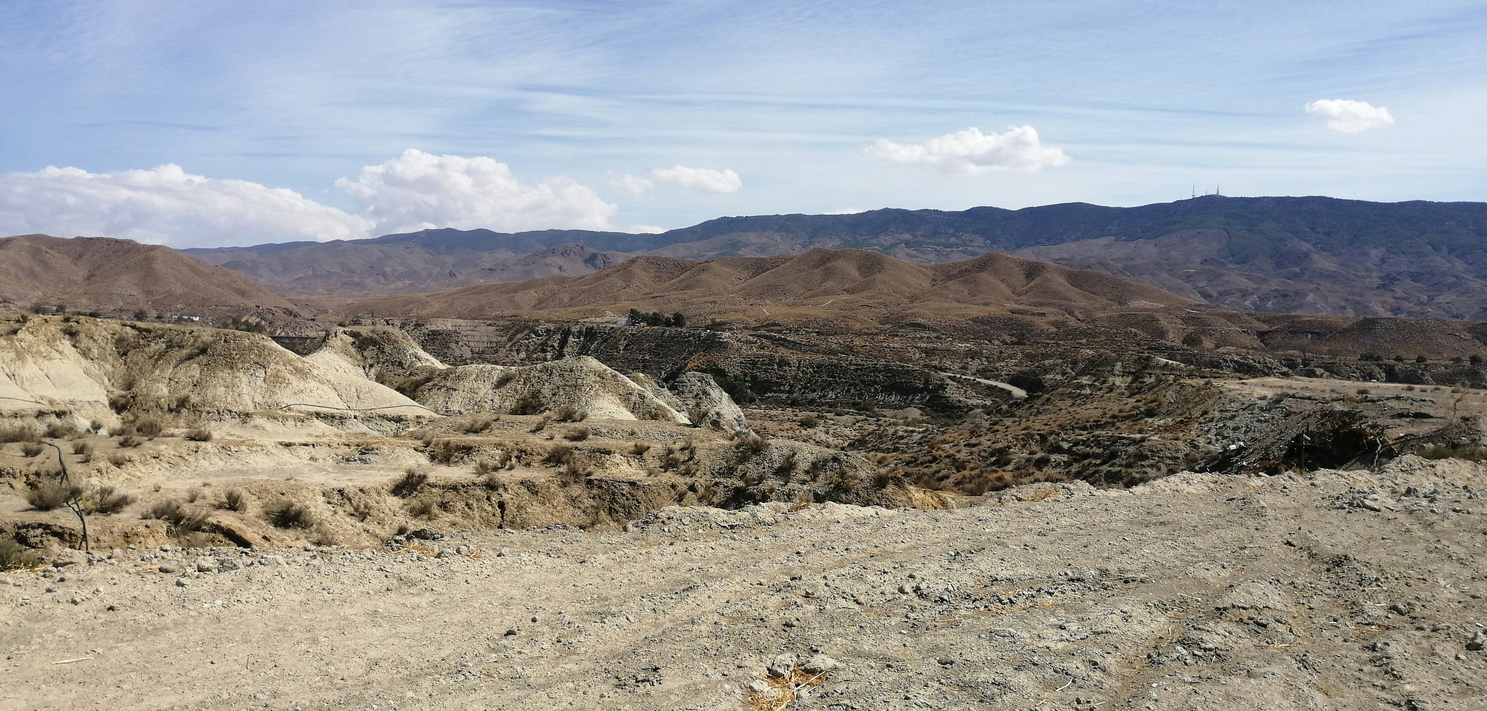 Arid landscape with rolling hills and distant mountains beneath a clear blue sky.