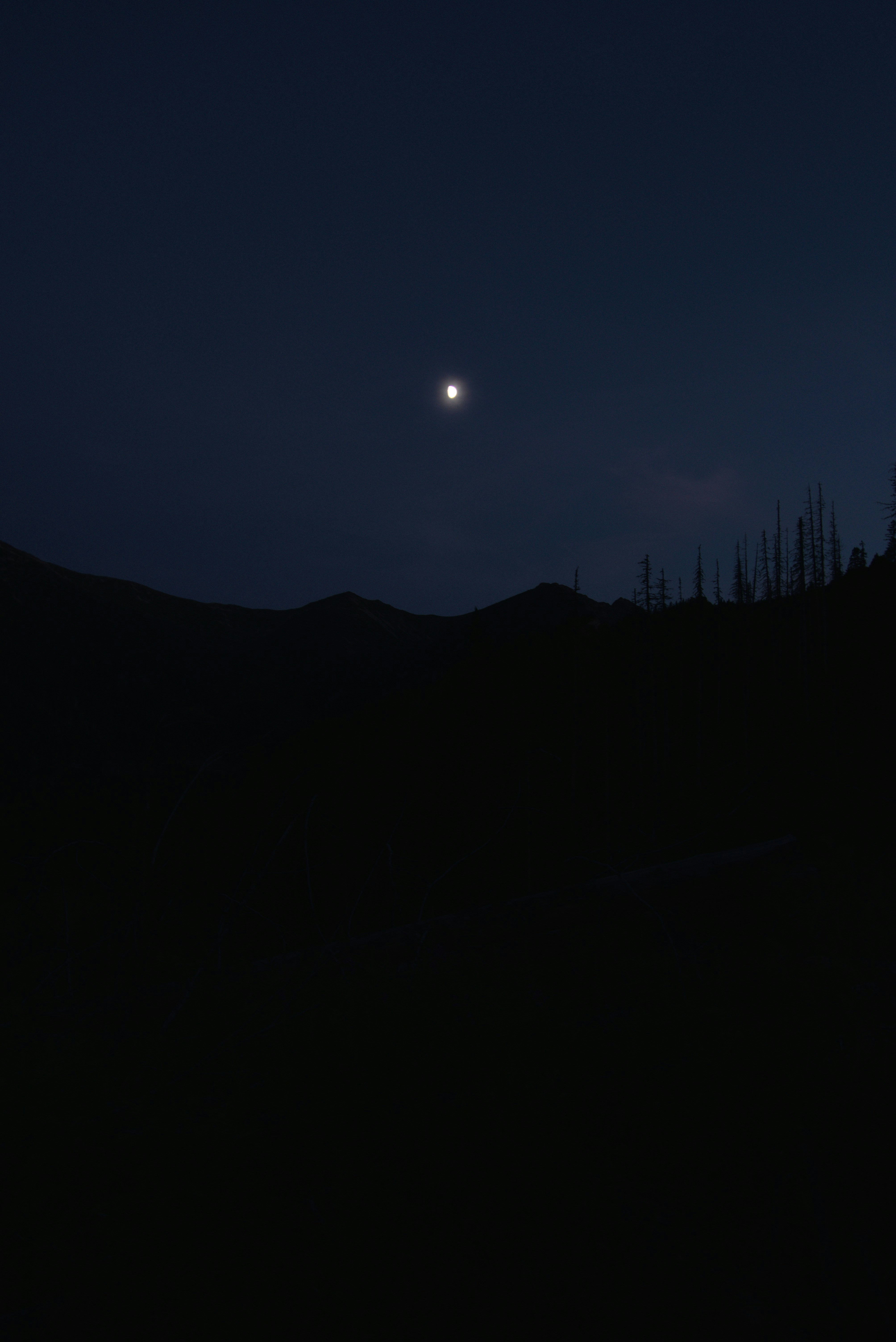 A solitary moon illuminates the dark silhouette of mountains, creating a serene and mysterious atmosphere.