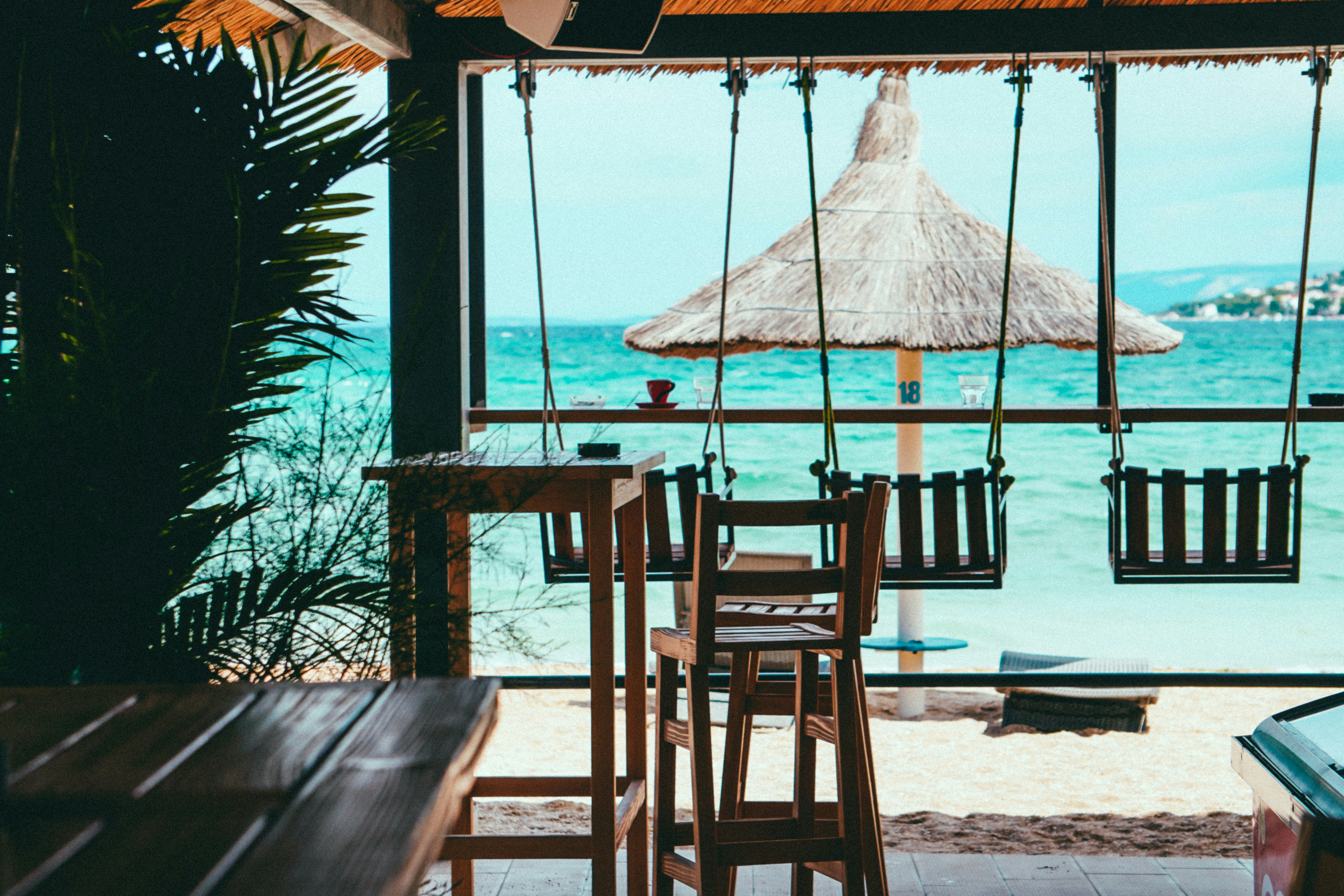 Beachfront café with wooden swings and ocean view under a straw umbrella.