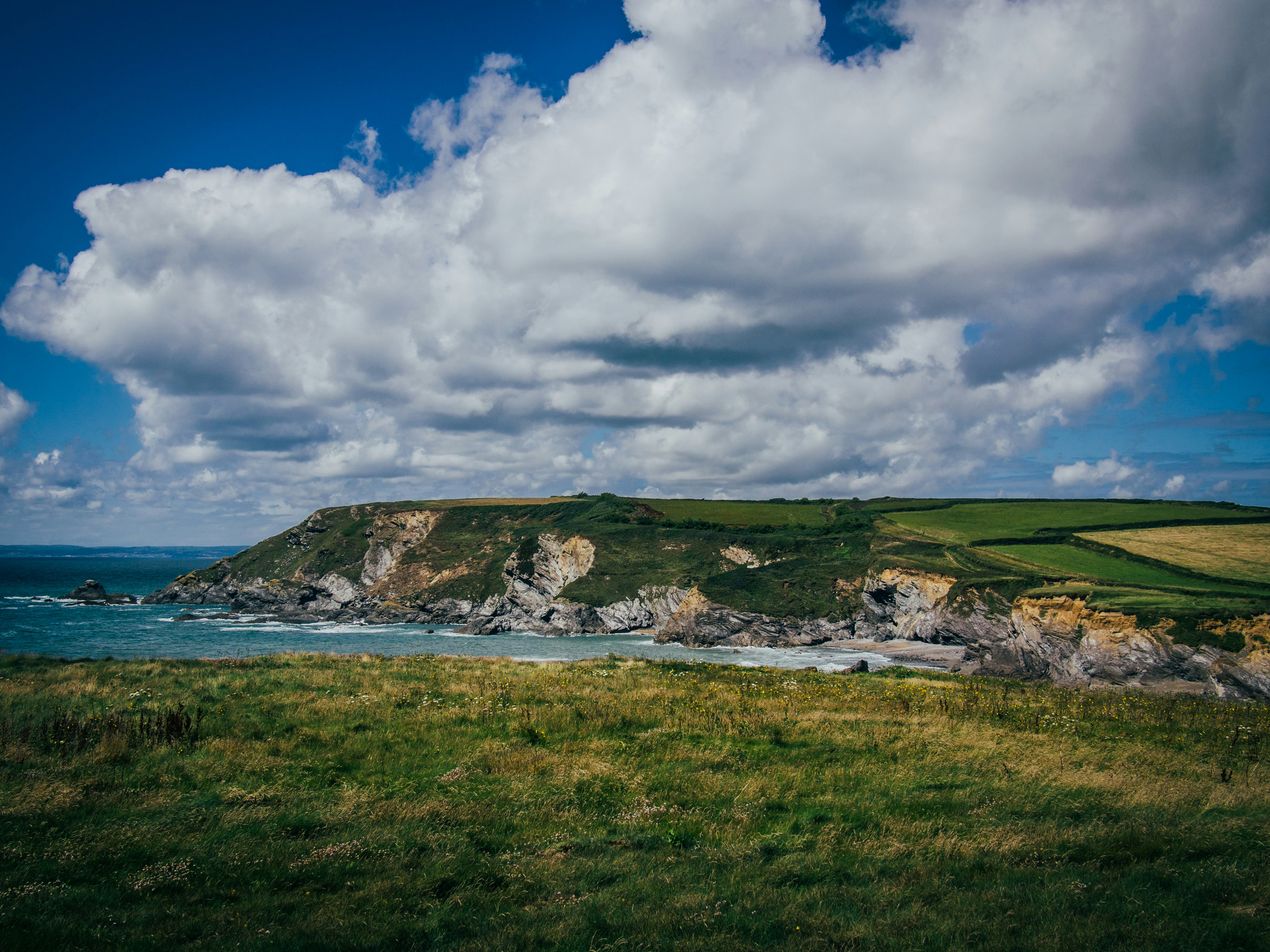 Vibrant green fields blend seamlessly with rugged cliffs and a turquoise sea under a dynamic sky filled with clouds.