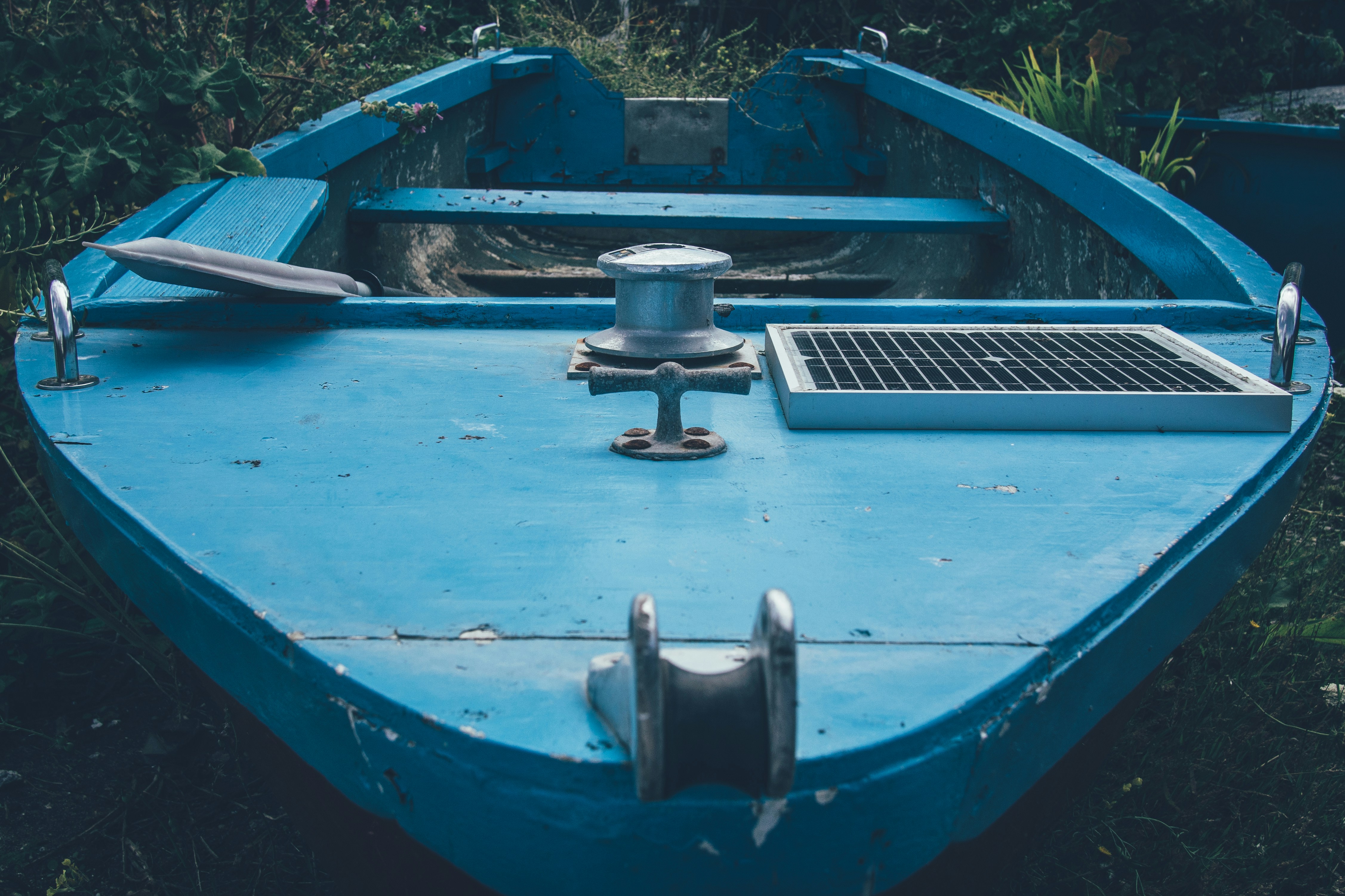 Weathered blue boat resting amidst greenery, showcasing its rustic charm and nautical elements.