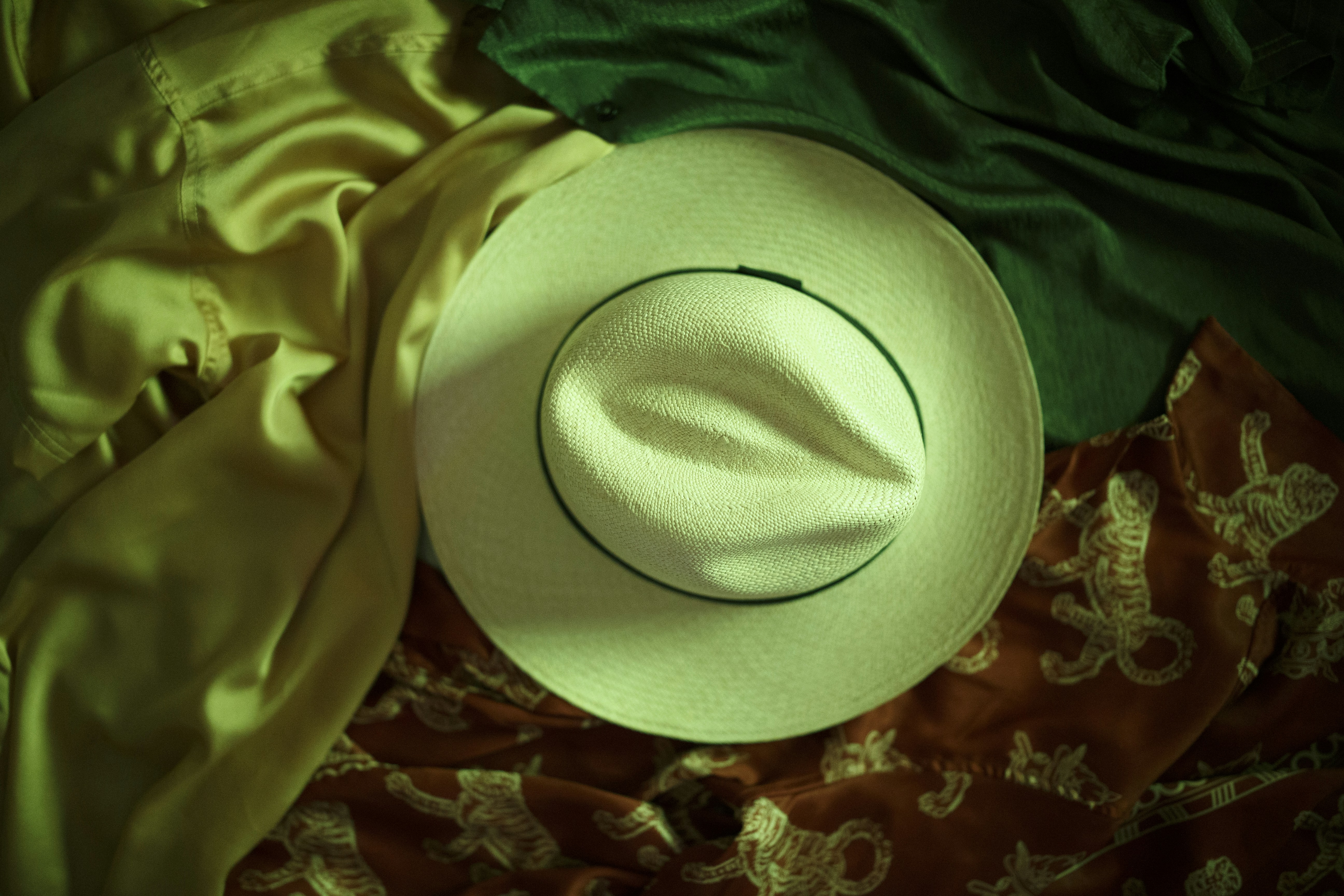 Wide-brimmed straw hat resting atop a colorful arrangement of fabrics, showcasing a blend of textures and hues.