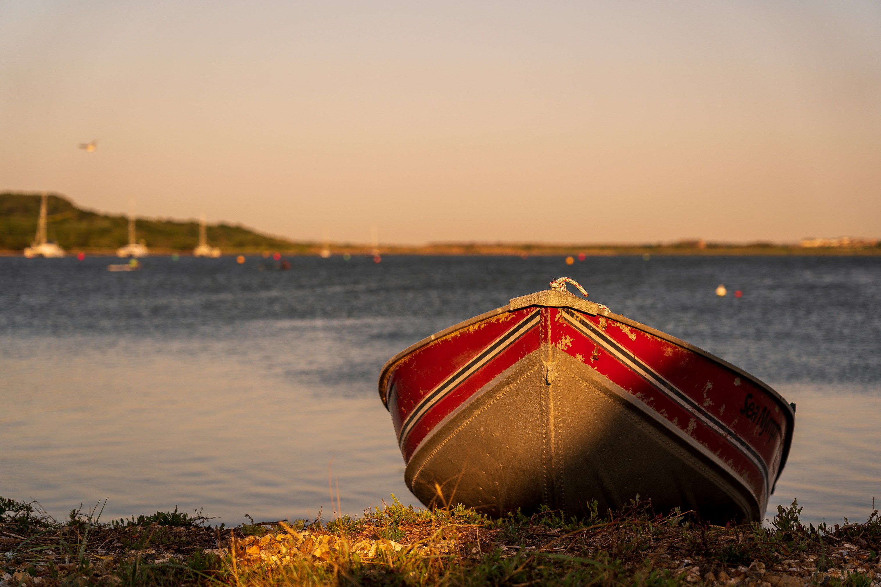 A colorful boat rests on the shore, reflecting the calm waters of the harbor under a warm sunset glow.
