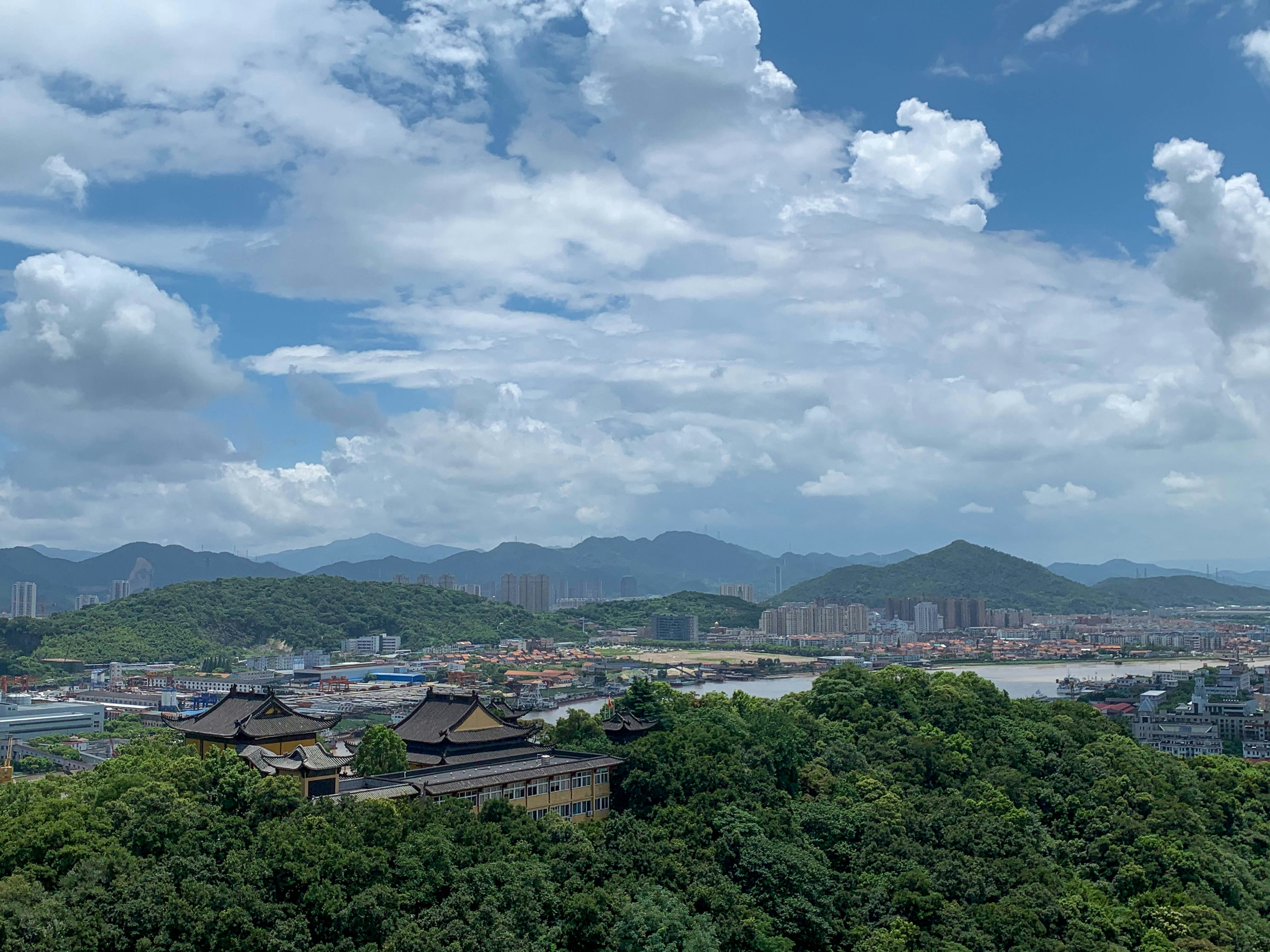 Traditional architecture nestled among lush greenery with mountains and a cloudy sky in the background.