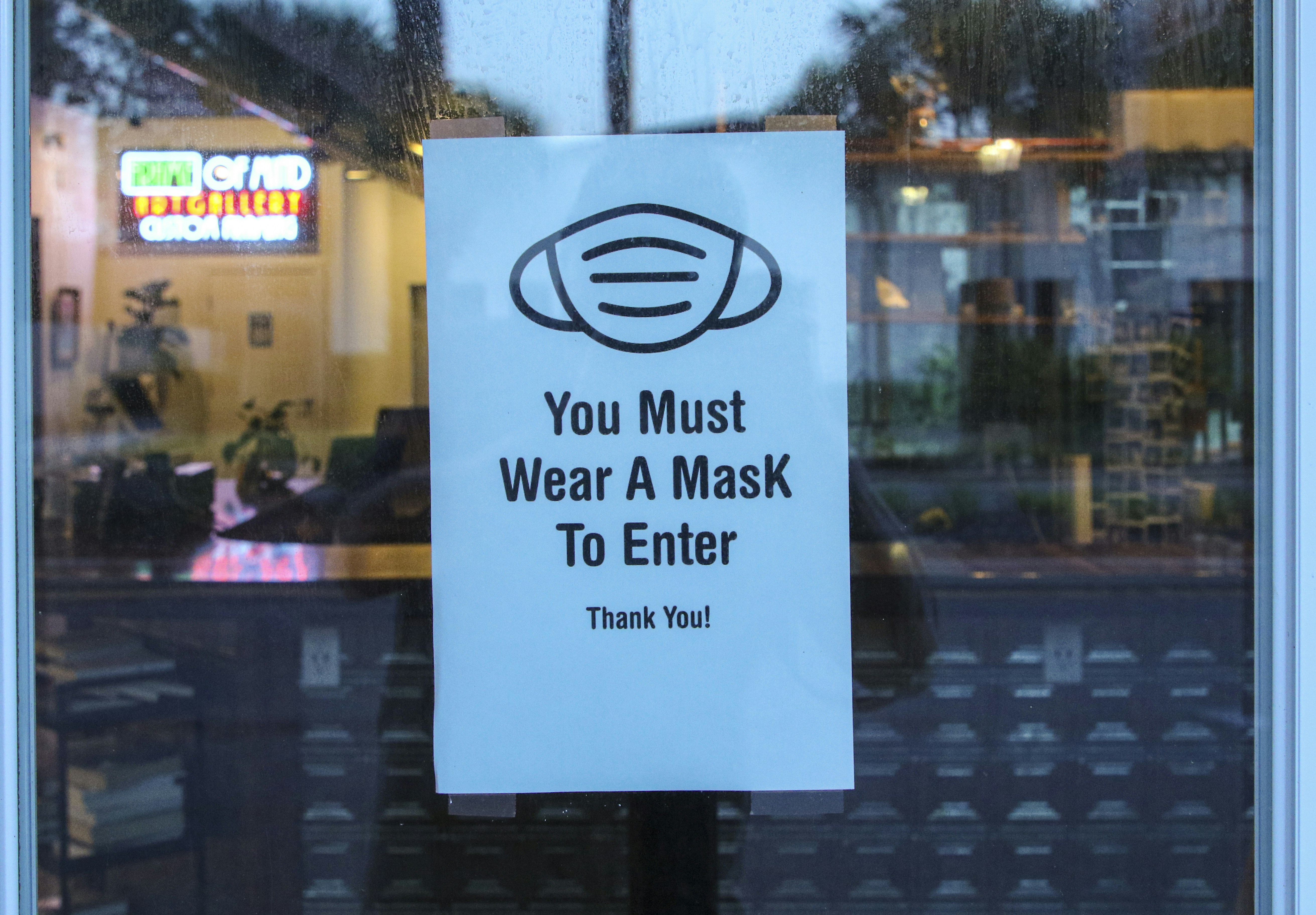 Sign on a glass door instructing visitors to wear a mask before entry.