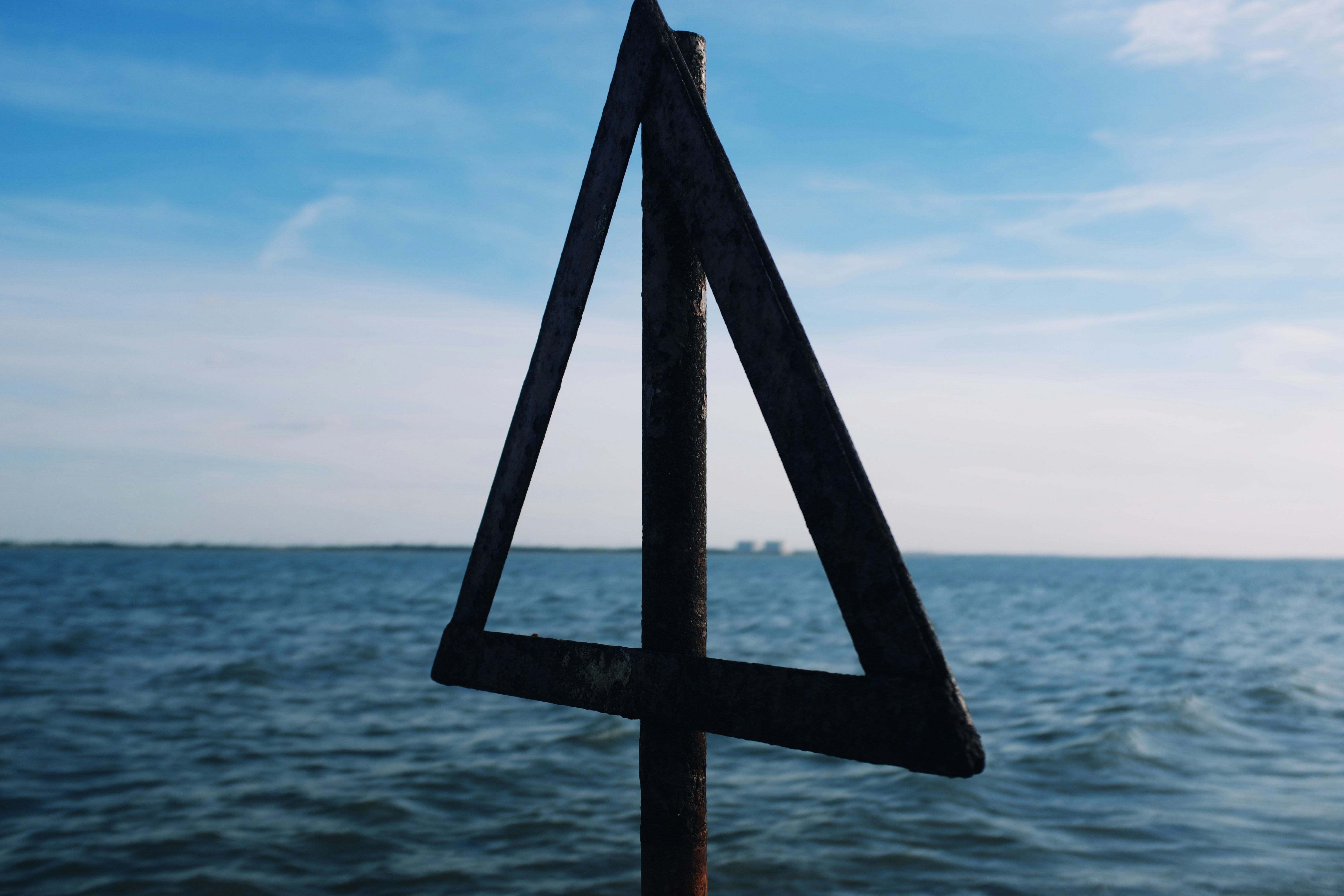 Metal marker in the shape of a triangle stands prominently against a backdrop of tranquil water and a clear sky.