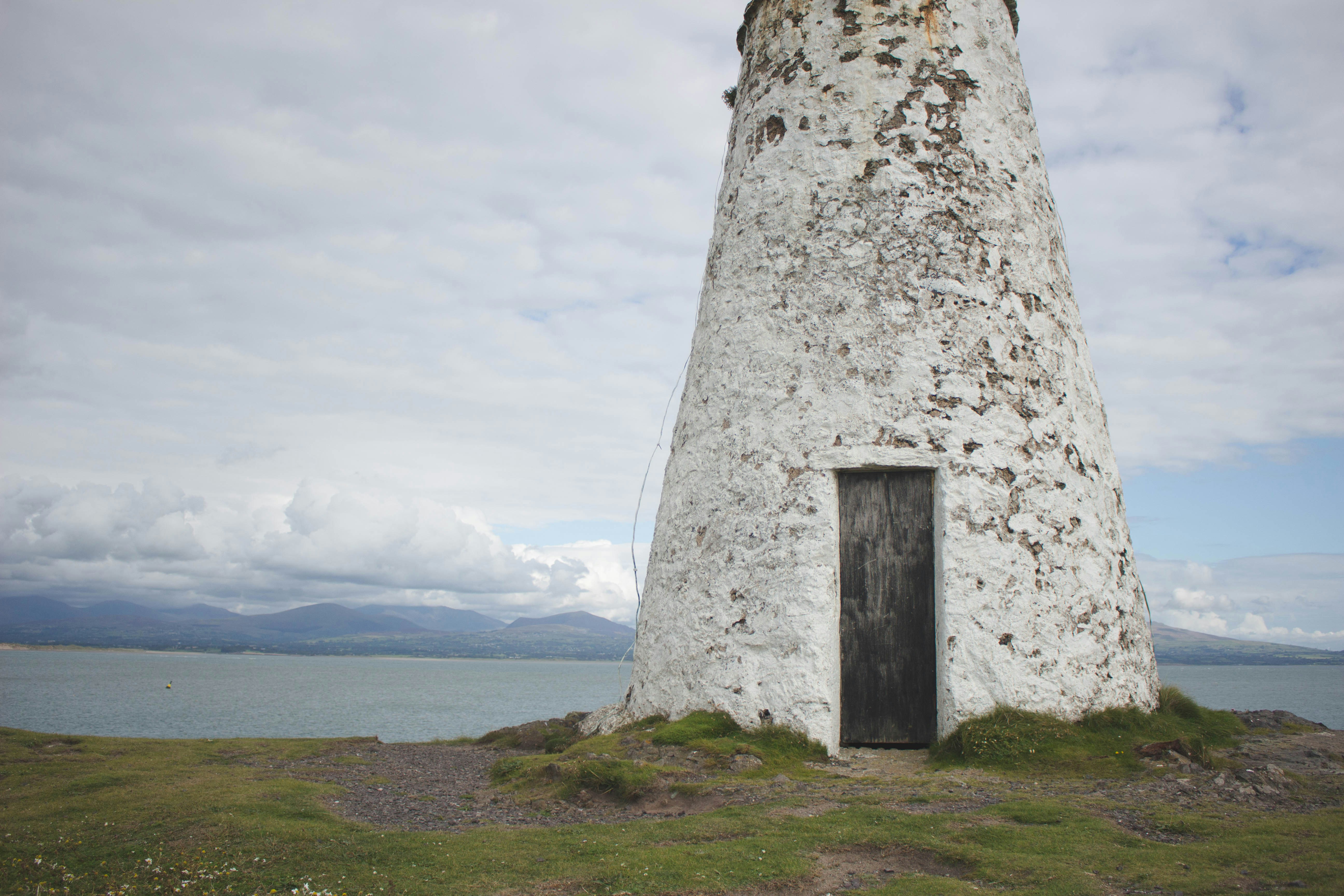 Weathered white tower by the sea: a solitary door against a moody, cloud-swept horizon.