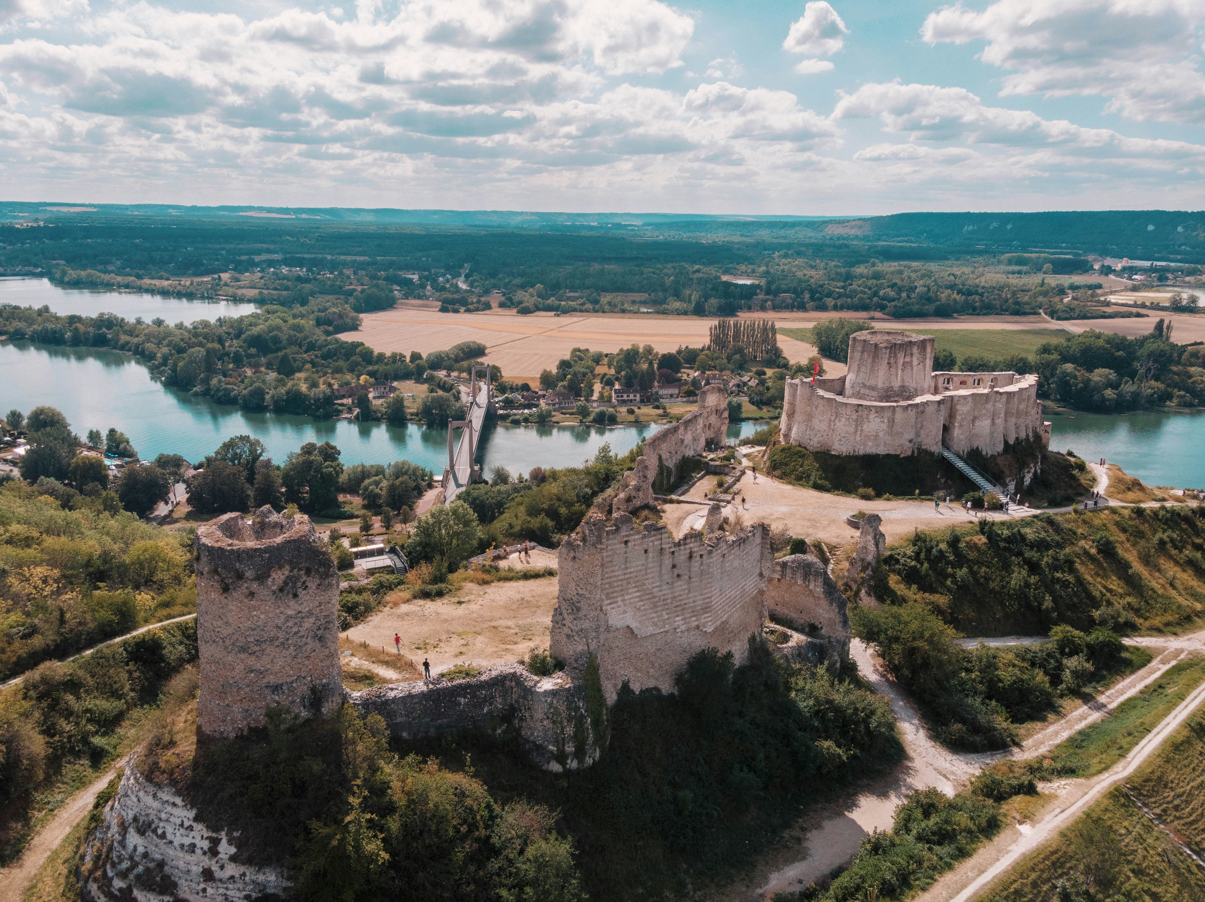 Ancient stone castle ruins surrounded by lush greenery near a winding river under a partly cloudy sky.