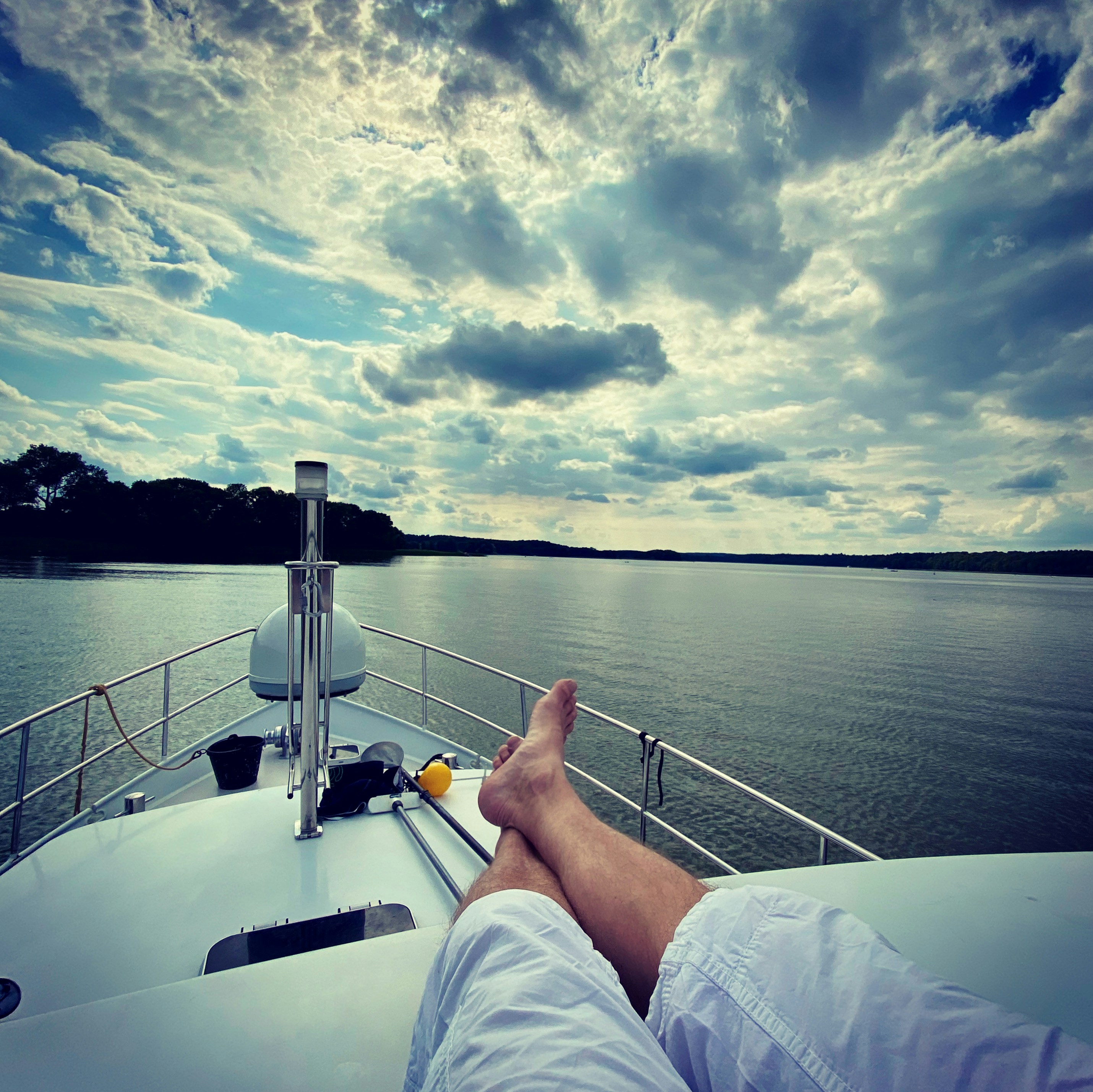 Feet resting on the bow of a boat, overlooking a calm river under a dramatic sky filled with clouds.