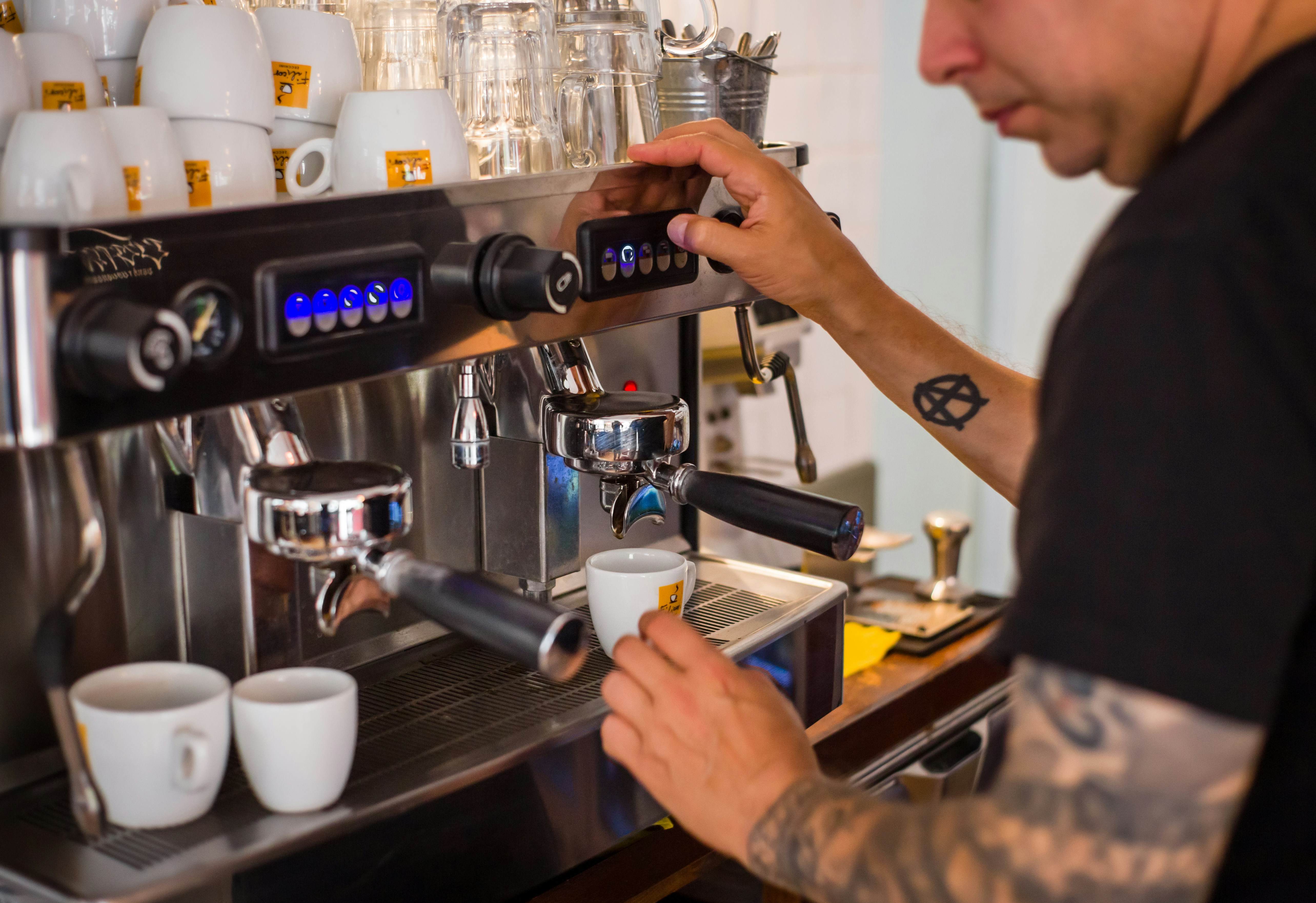 Barista preparing coffee with a professional espresso machine, surrounded by cups and tools.