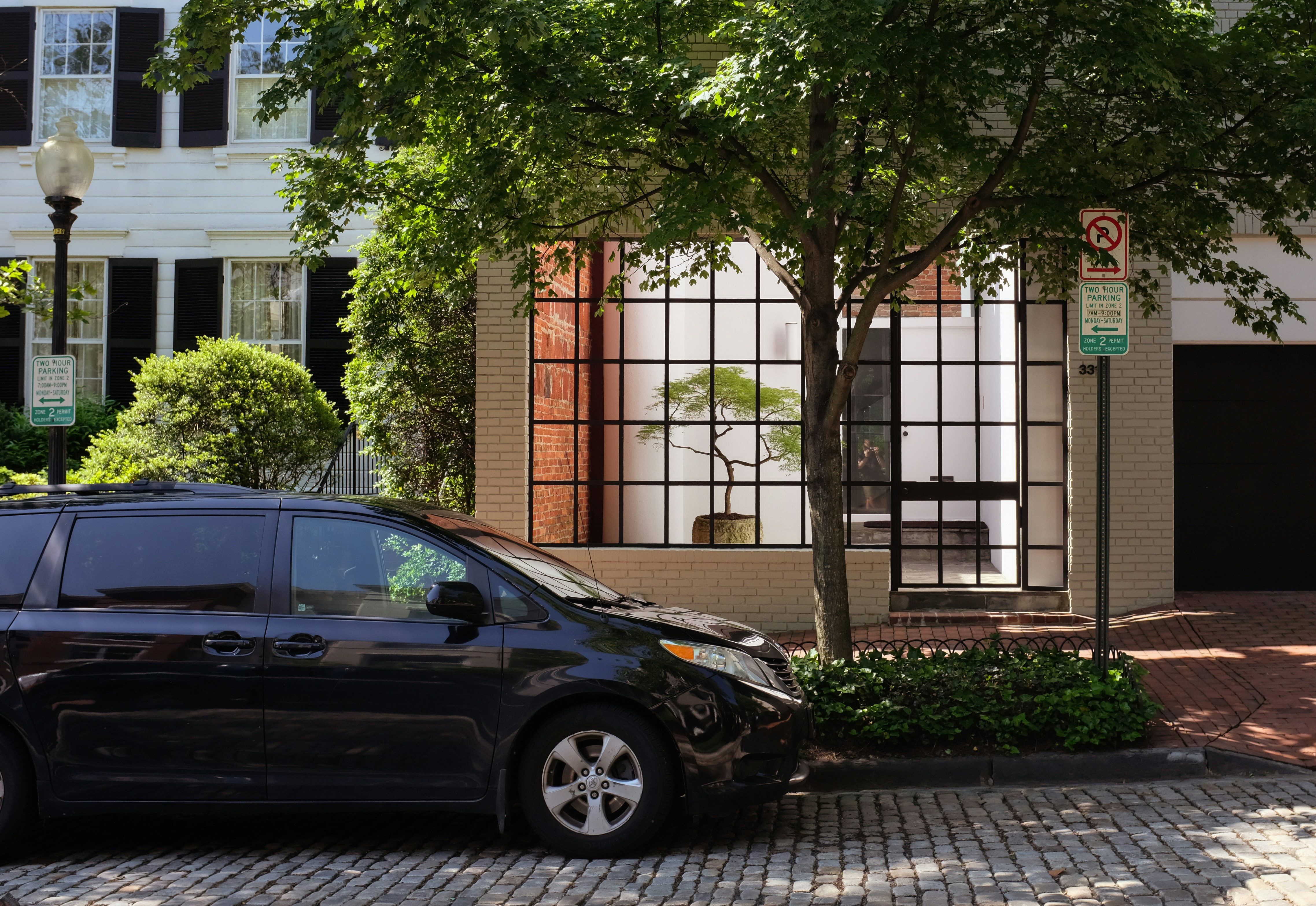 A sleek black minivan parked beside a modern glass facade, framed by lush greenery and urban architecture. The scene captures a harmonious blend of nature and contemporary design.
