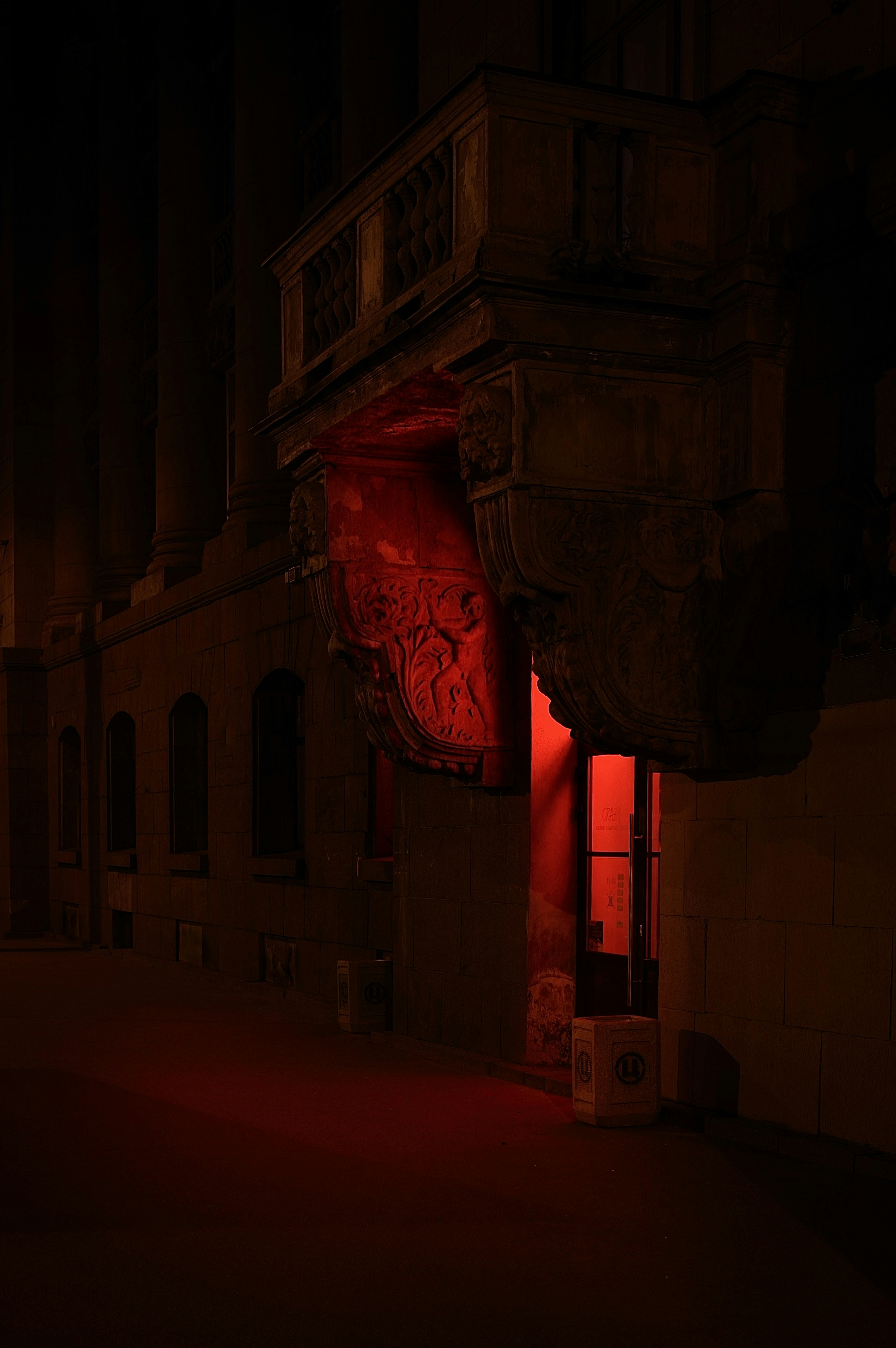 Illuminated architectural feature casts a striking red hue against the darkened building, hinting at hidden stories within.