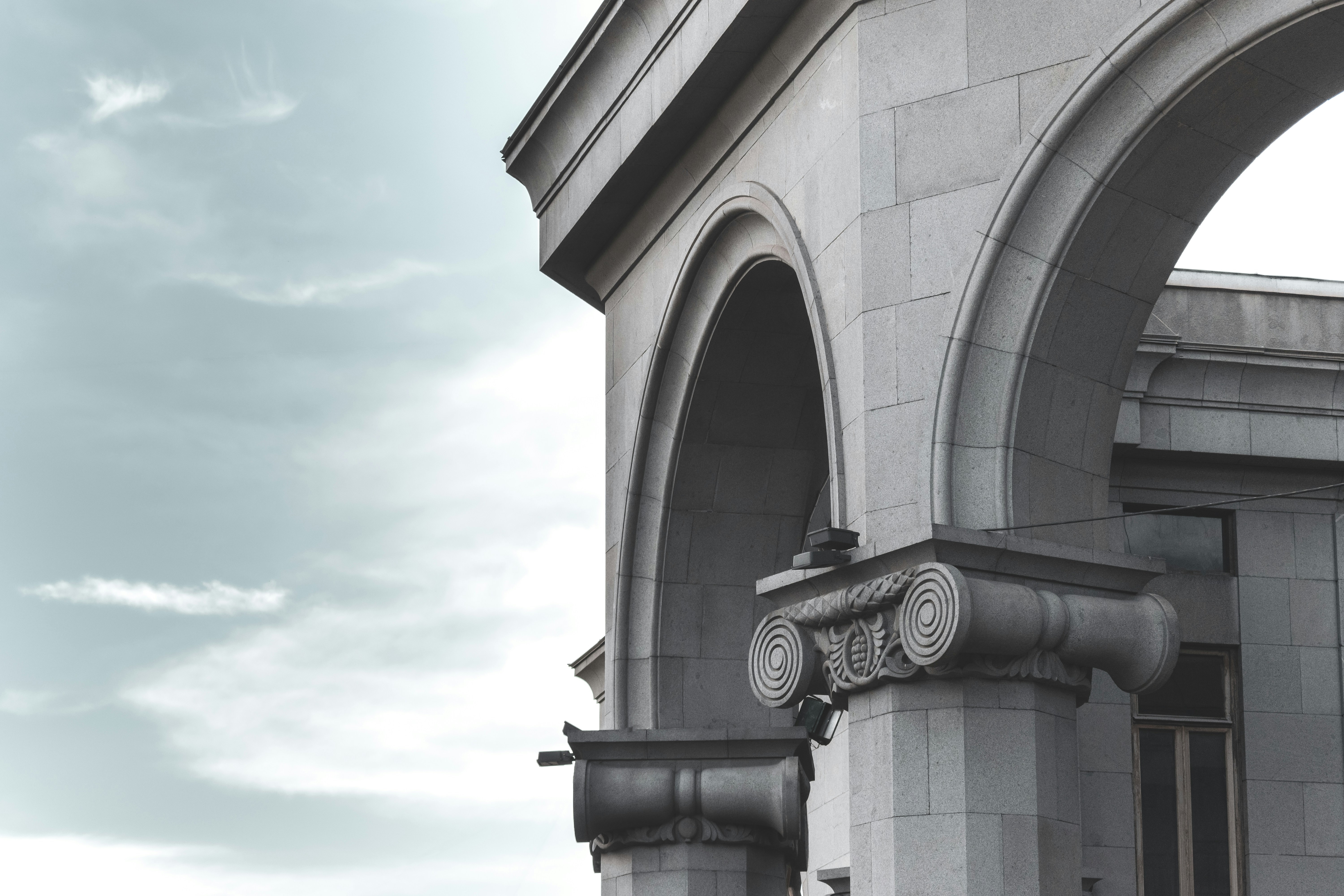 Classical stone archway with intricate detailing set against a pale blue sky.
