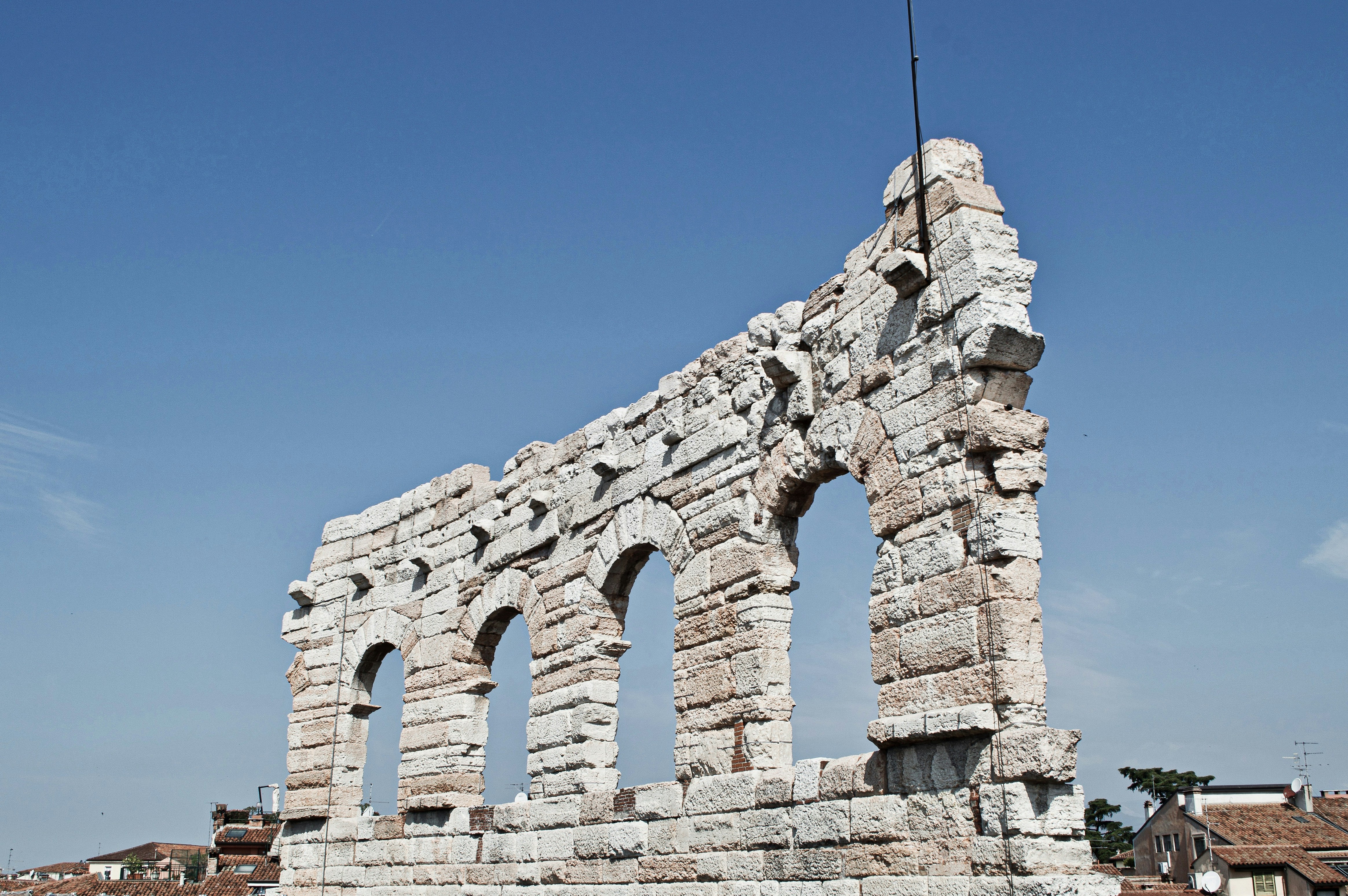Stone arch ruins with multiple openings stand against a bright blue sky.