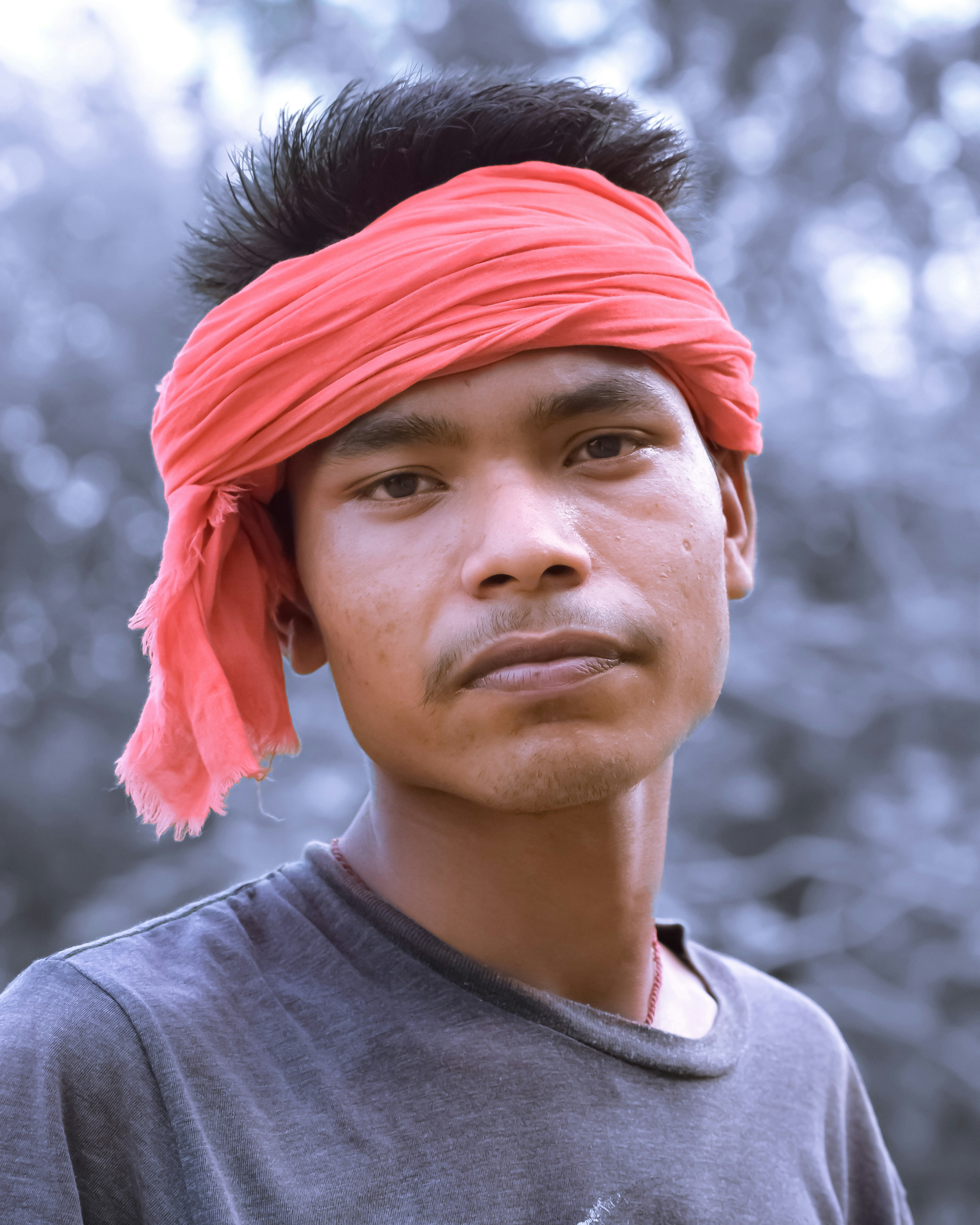 Young man wearing a vibrant red headband, gazing thoughtfully in a blurred natural setting.