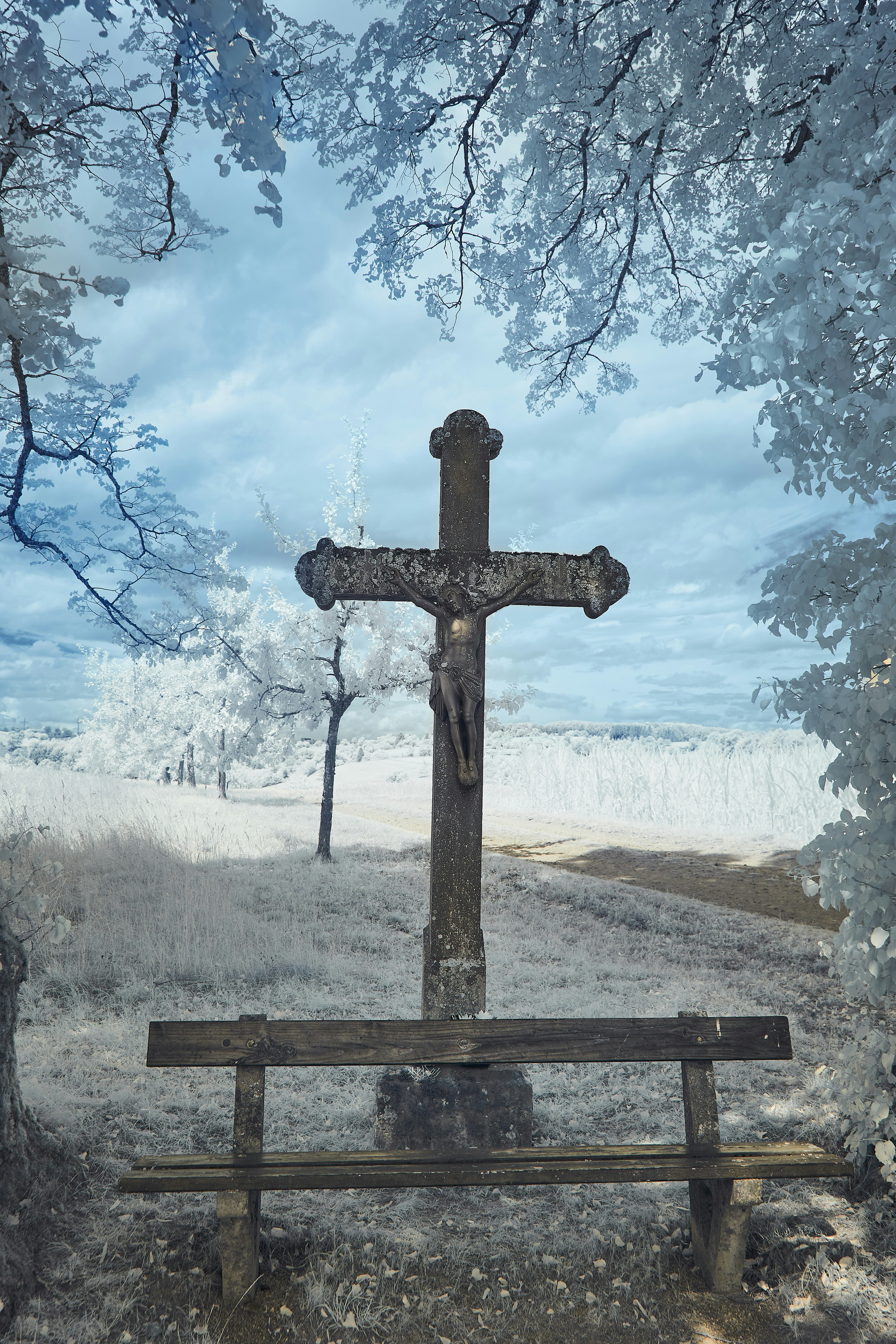 Cruciform Sentinel in Indigo Field: A Weathered Cross Framed by a Quiet Bench