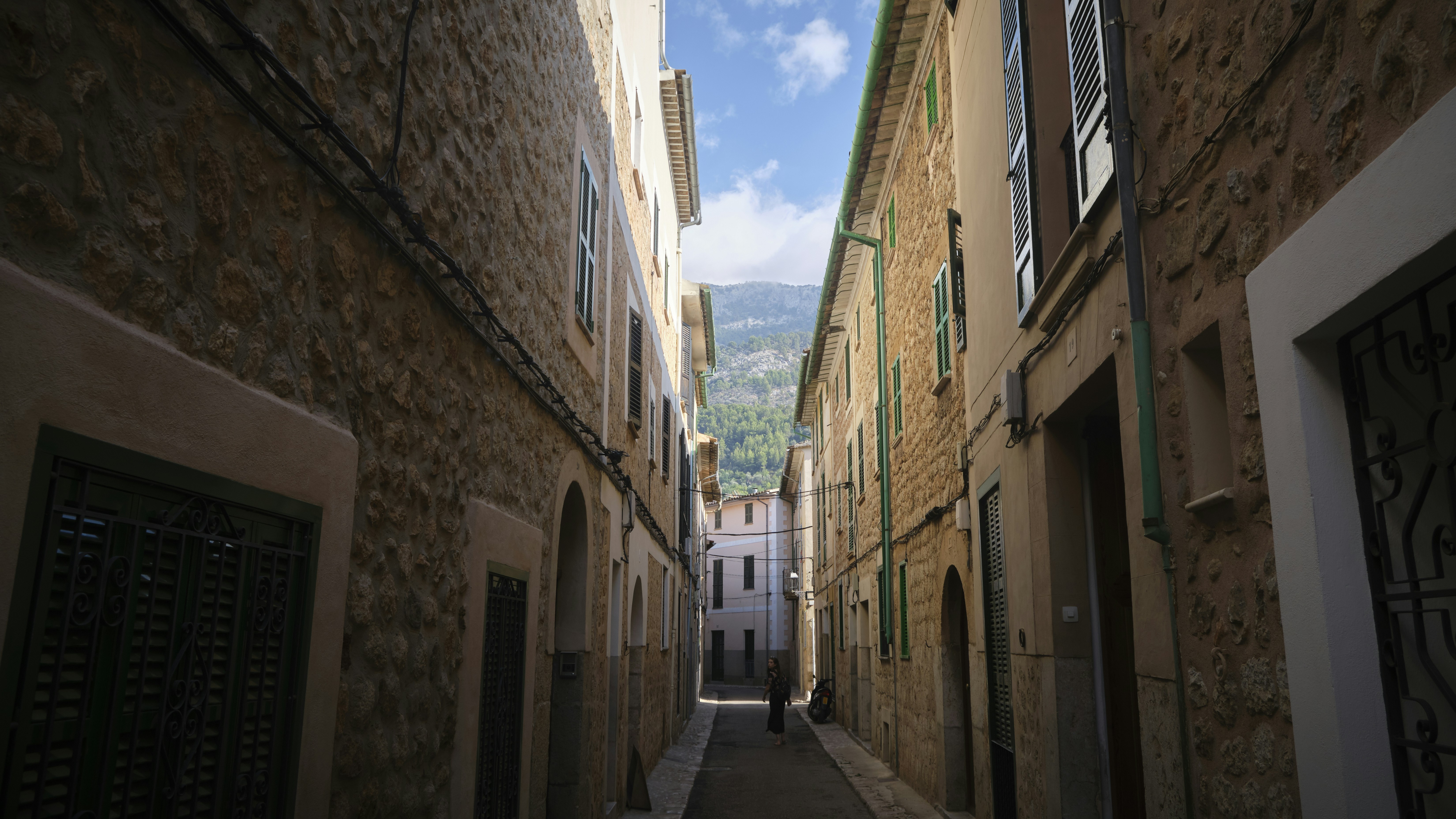 Narrow alley lined with rustic stone buildings under a bright blue sky.