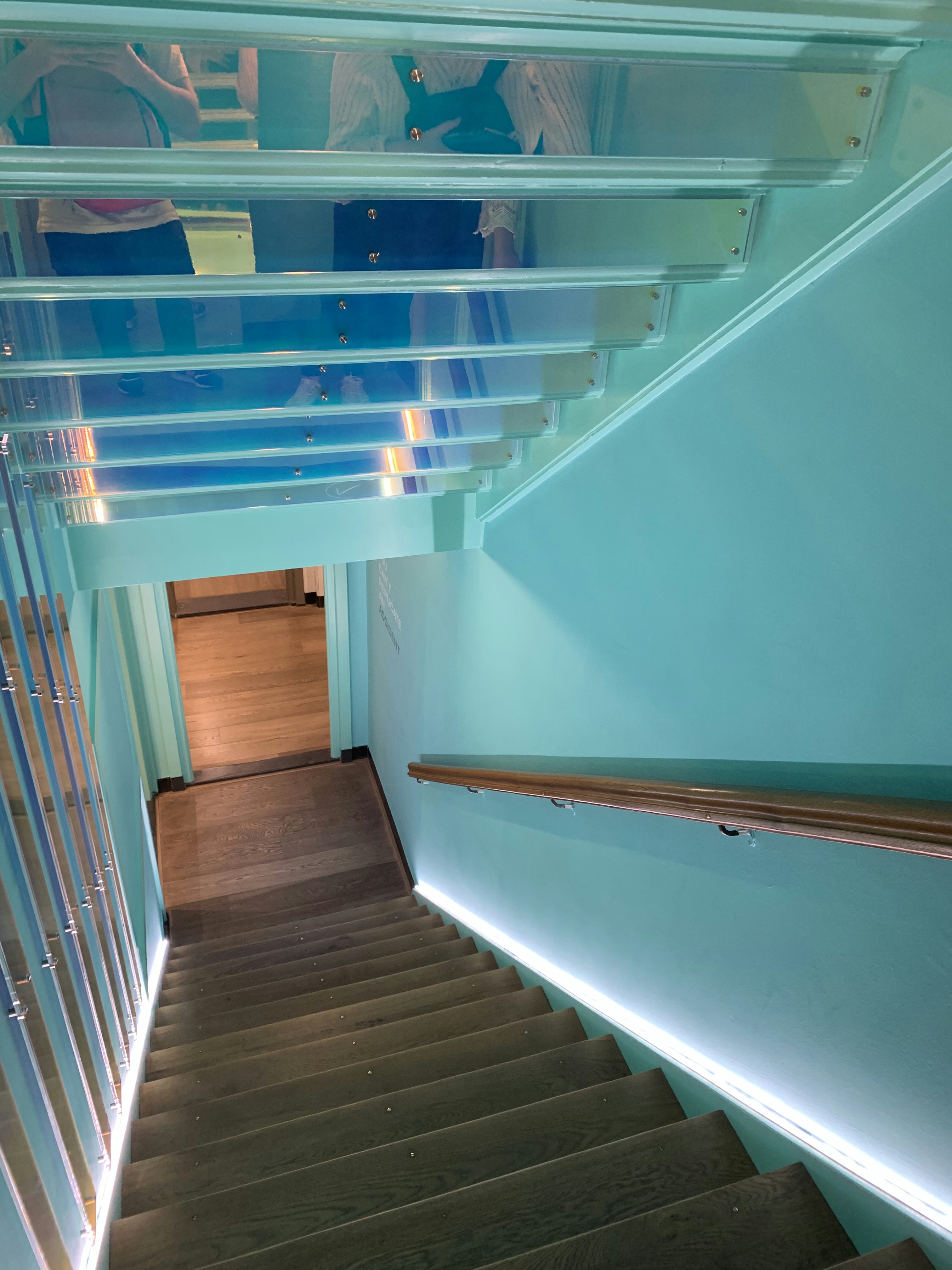 Stylish staircase with glass railings and soft lighting, leading to a doorway in a serene aqua-colored interior.