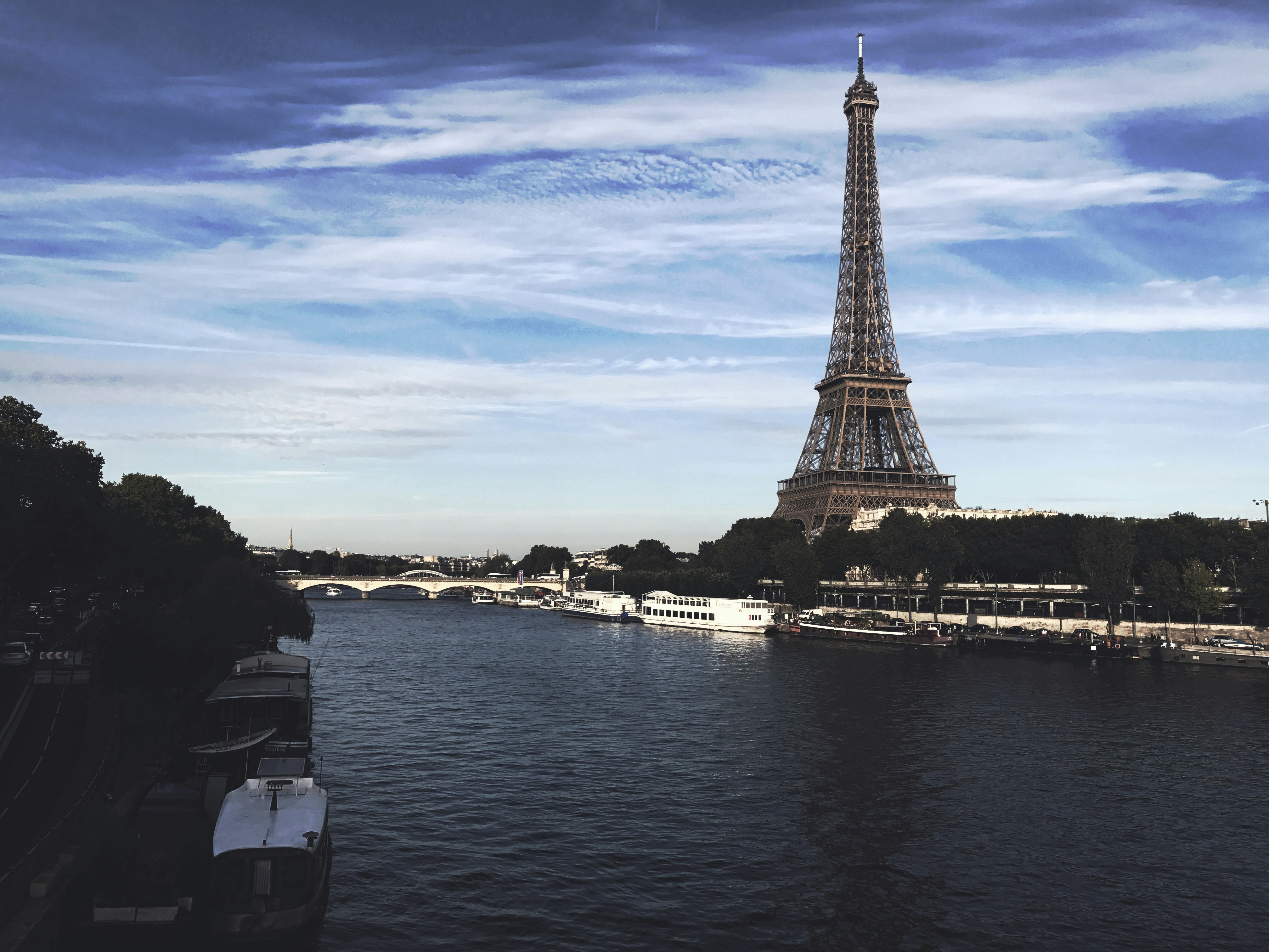 Eiffel Tower towering over the Seine River, framed by a serene sky and boats along the water's edge.