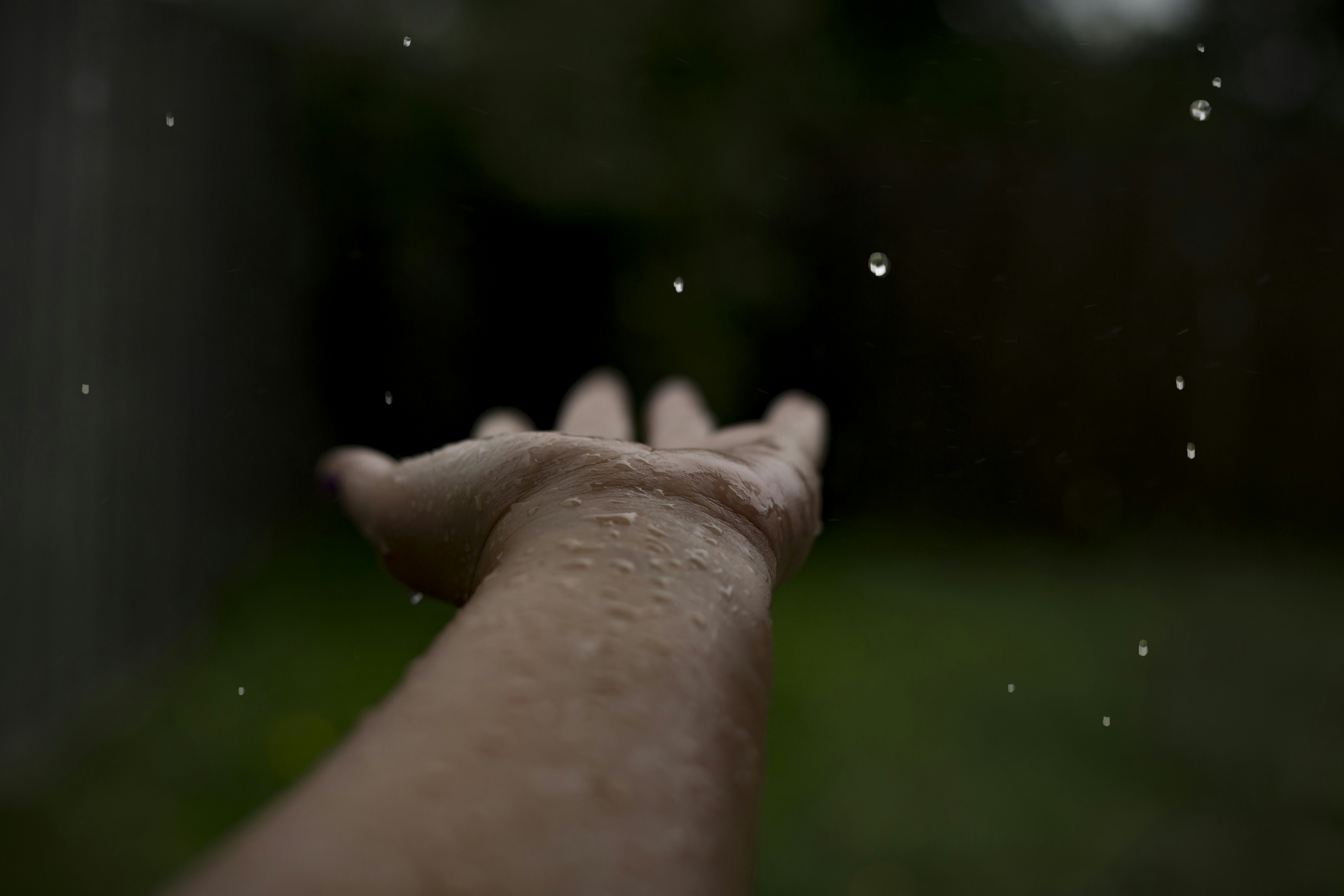 Outstretched hand catching raindrops against a blurred green backdrop.