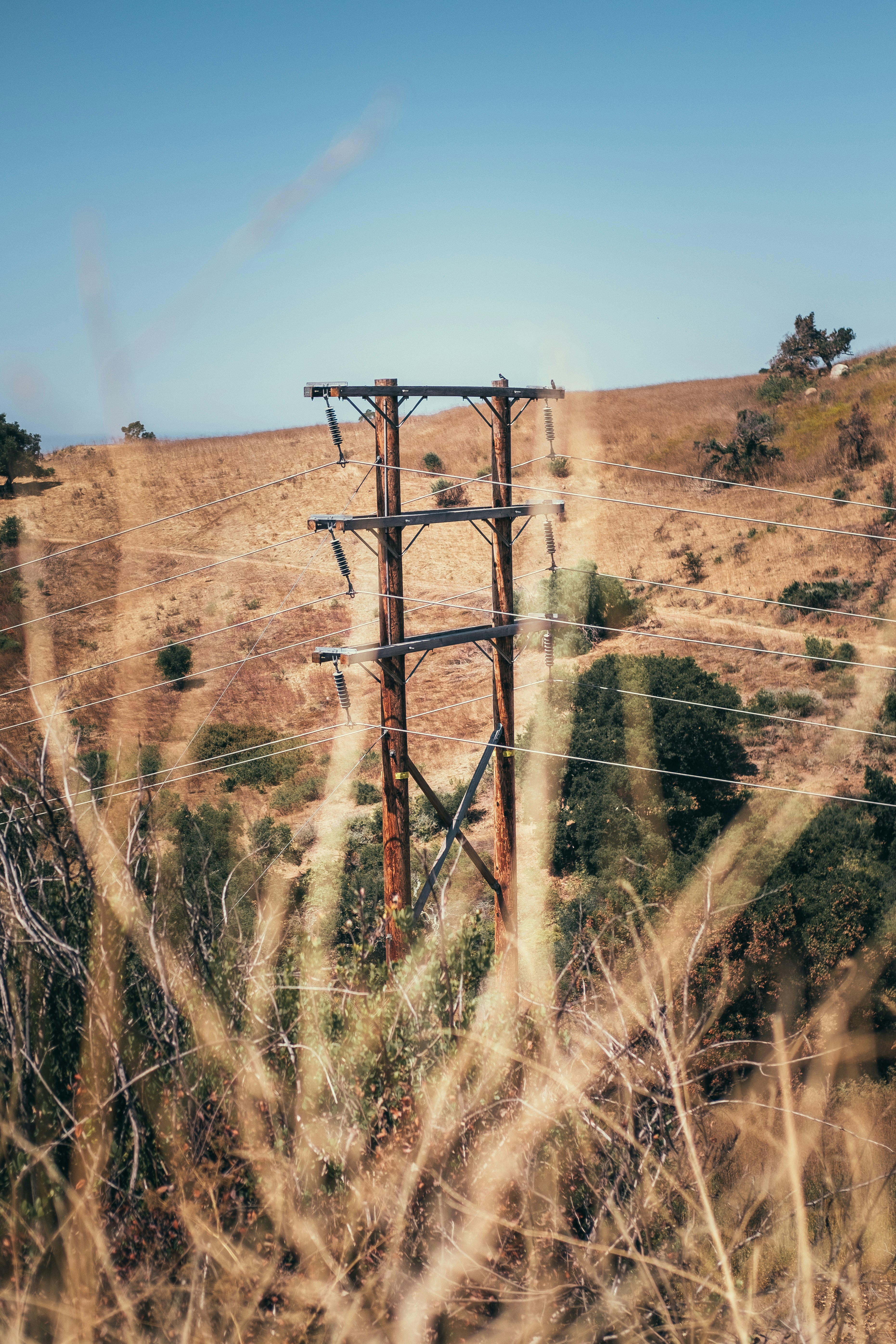 Weathered power lines stand tall against a backdrop of rolling hills and clear blue skies.