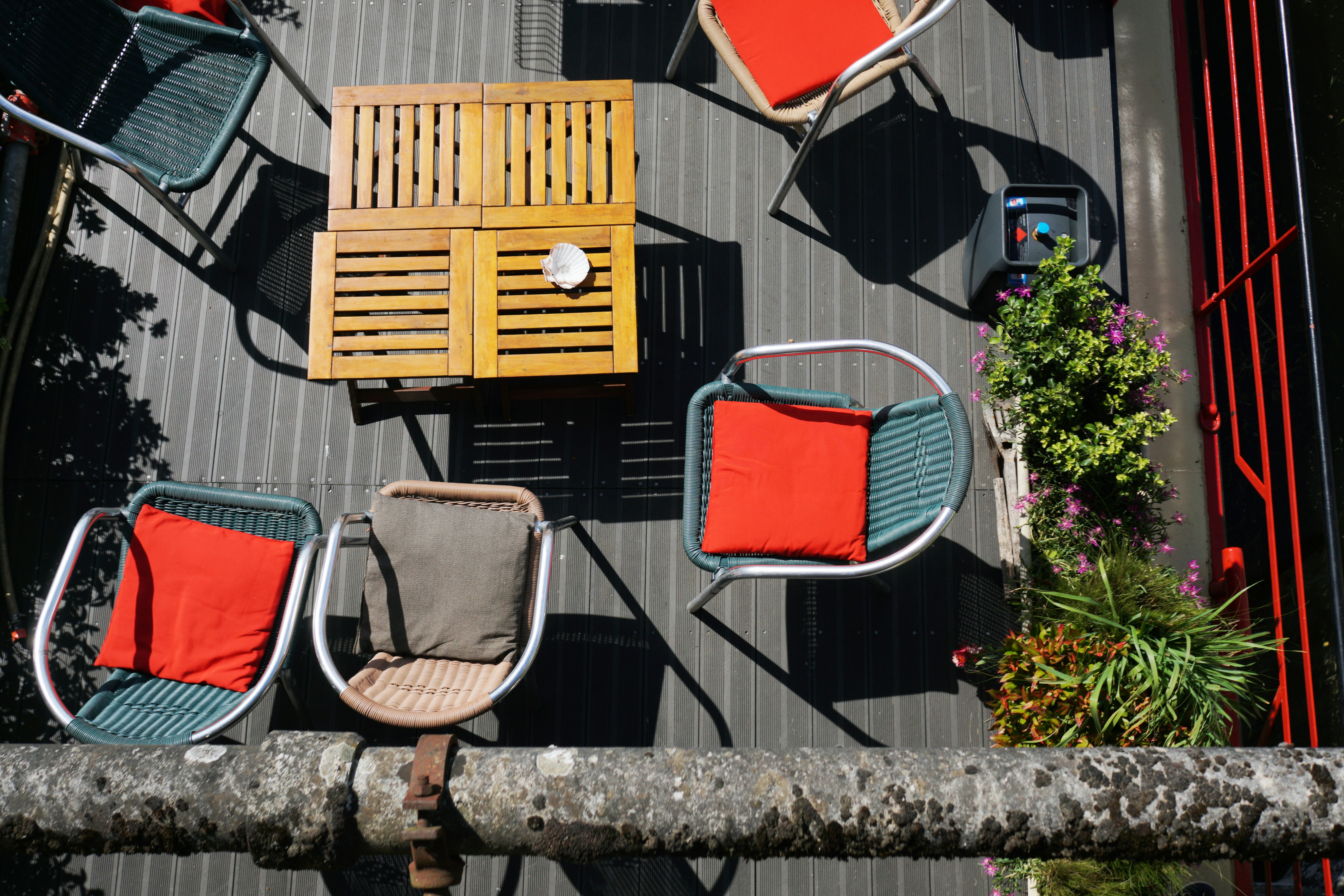 An inviting outdoor seating area featuring a wooden table surrounded by colorful chairs, with lush greenery and a coffee cup adding charm.