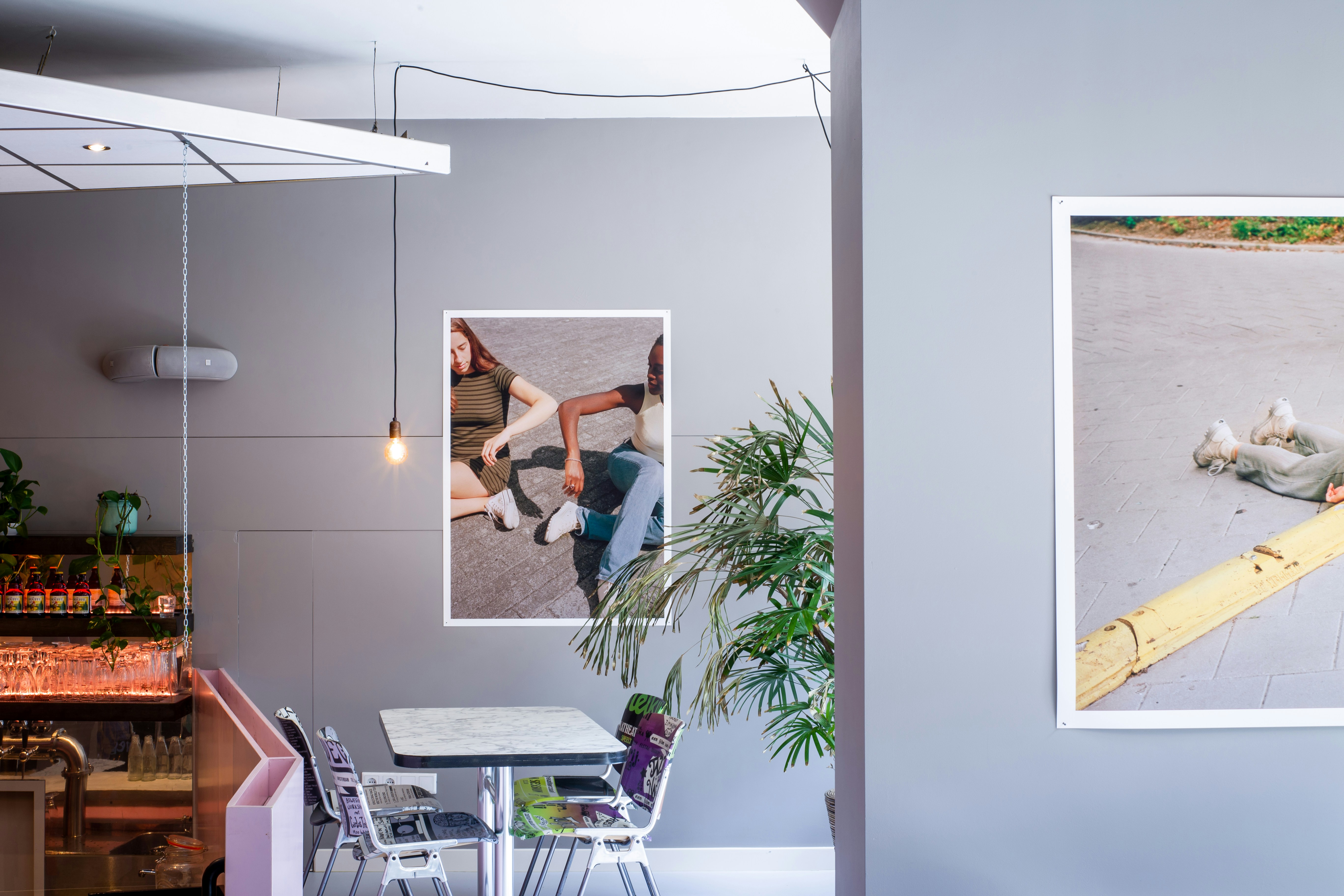 Contemporary cafe interior featuring eclectic wall art, a cozy seating area with transparent chairs, and vibrant greenery.