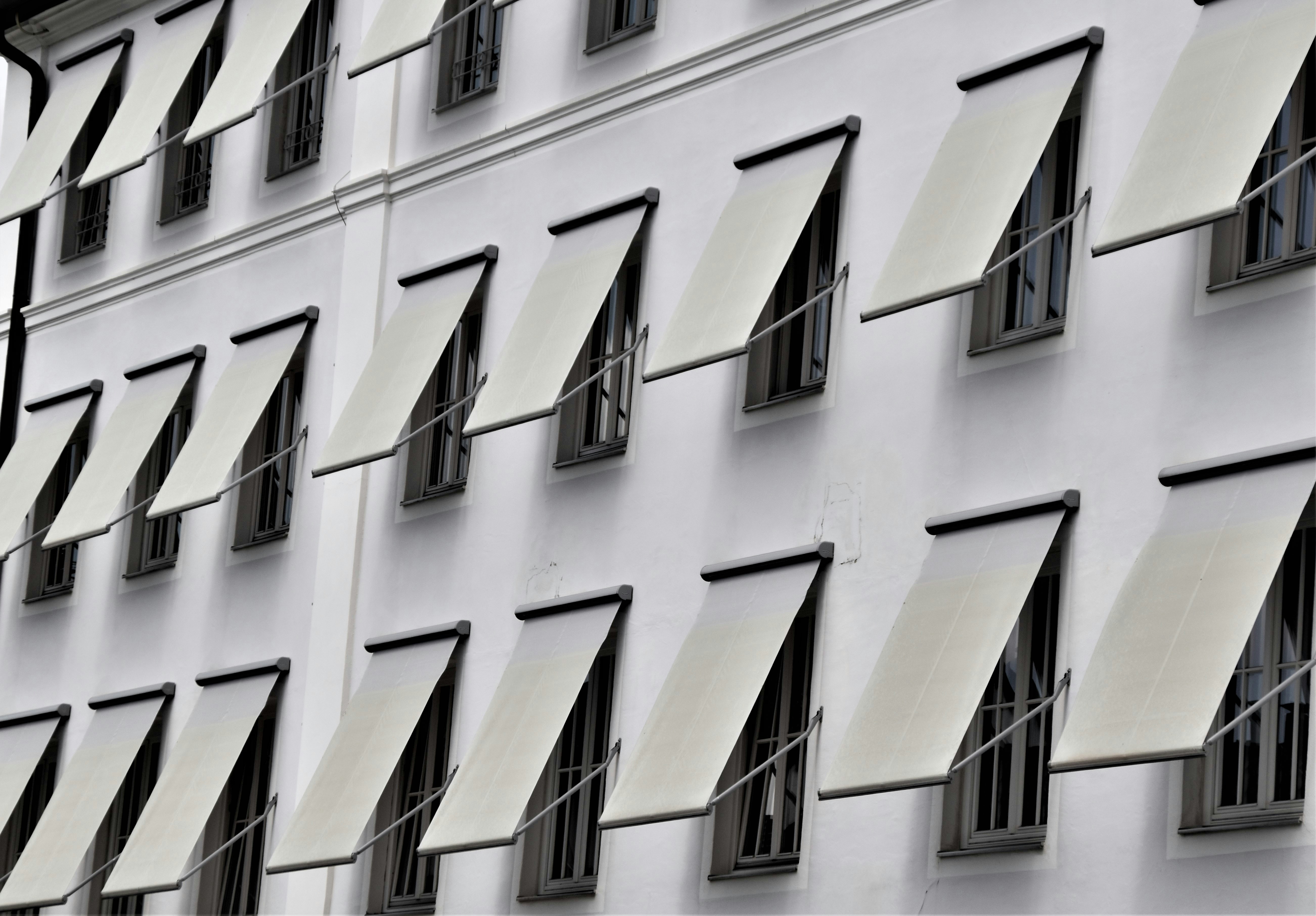 A series of fabric awnings gracefully adorn a white building facade, creating a rhythmic pattern of light and shadow.