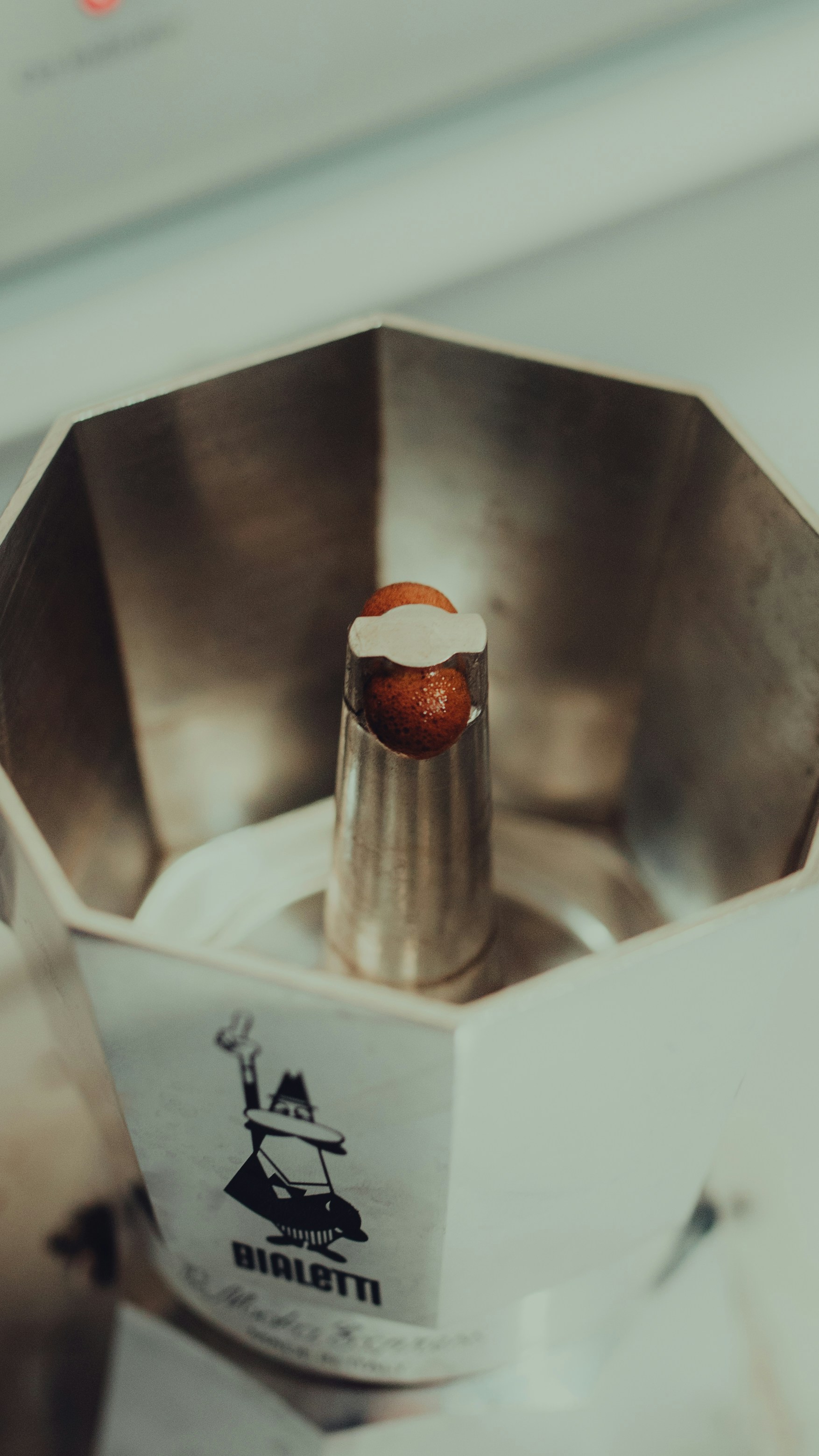 Close-up of a Bialetti espresso maker showcasing the coffee chamber and iconic logo. The copper-colored coffee ball rests at the center, ready for brewing.