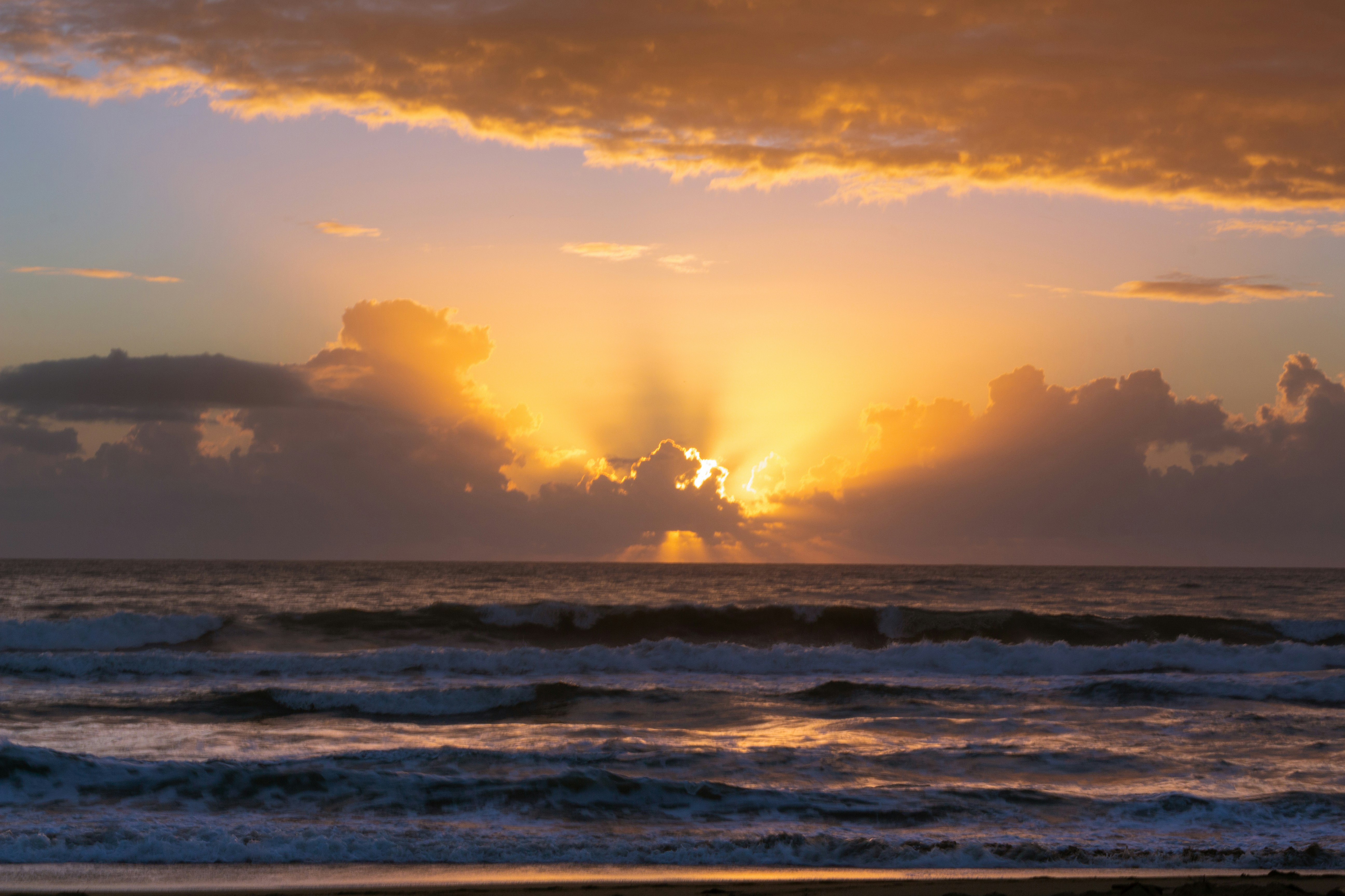 Golden sunrise with dramatic clouds casting rays over a calm ocean.