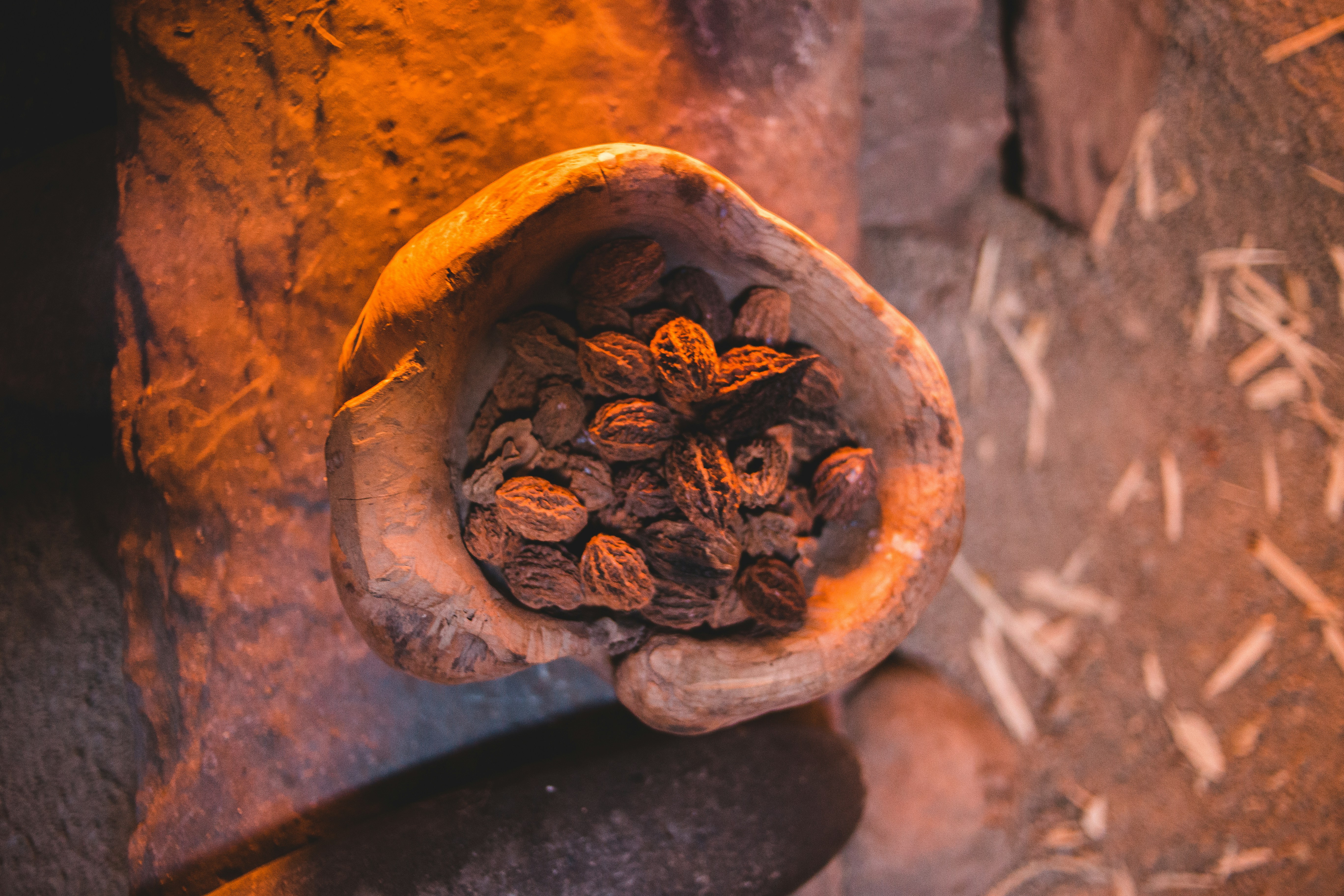 A rustic bowl filled with assorted nuts, illuminated by warm, ambient light, showcasing the textures of both the bowl and its contents.