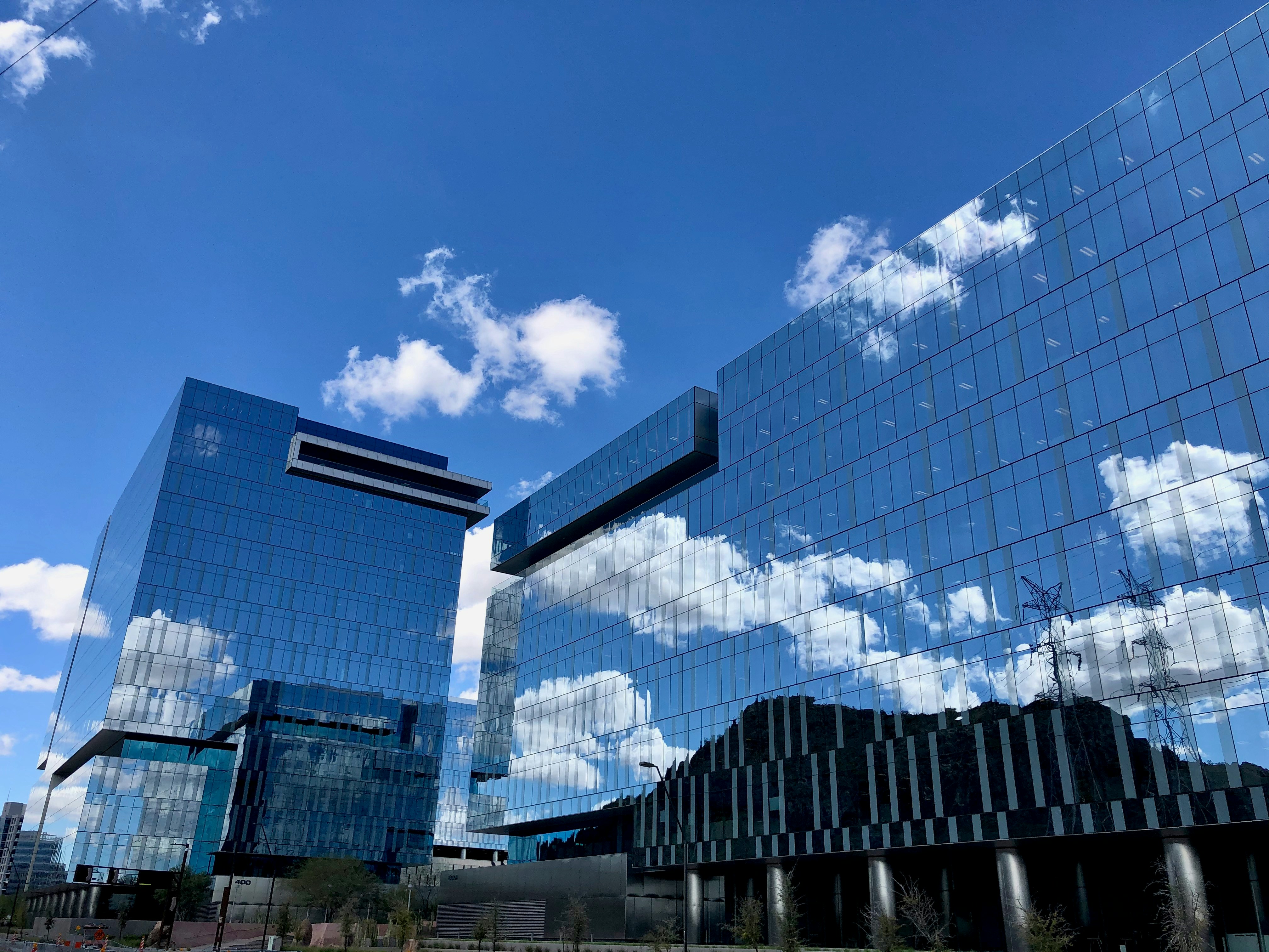 Modern glass buildings reflecting clouds against a bright blue sky.