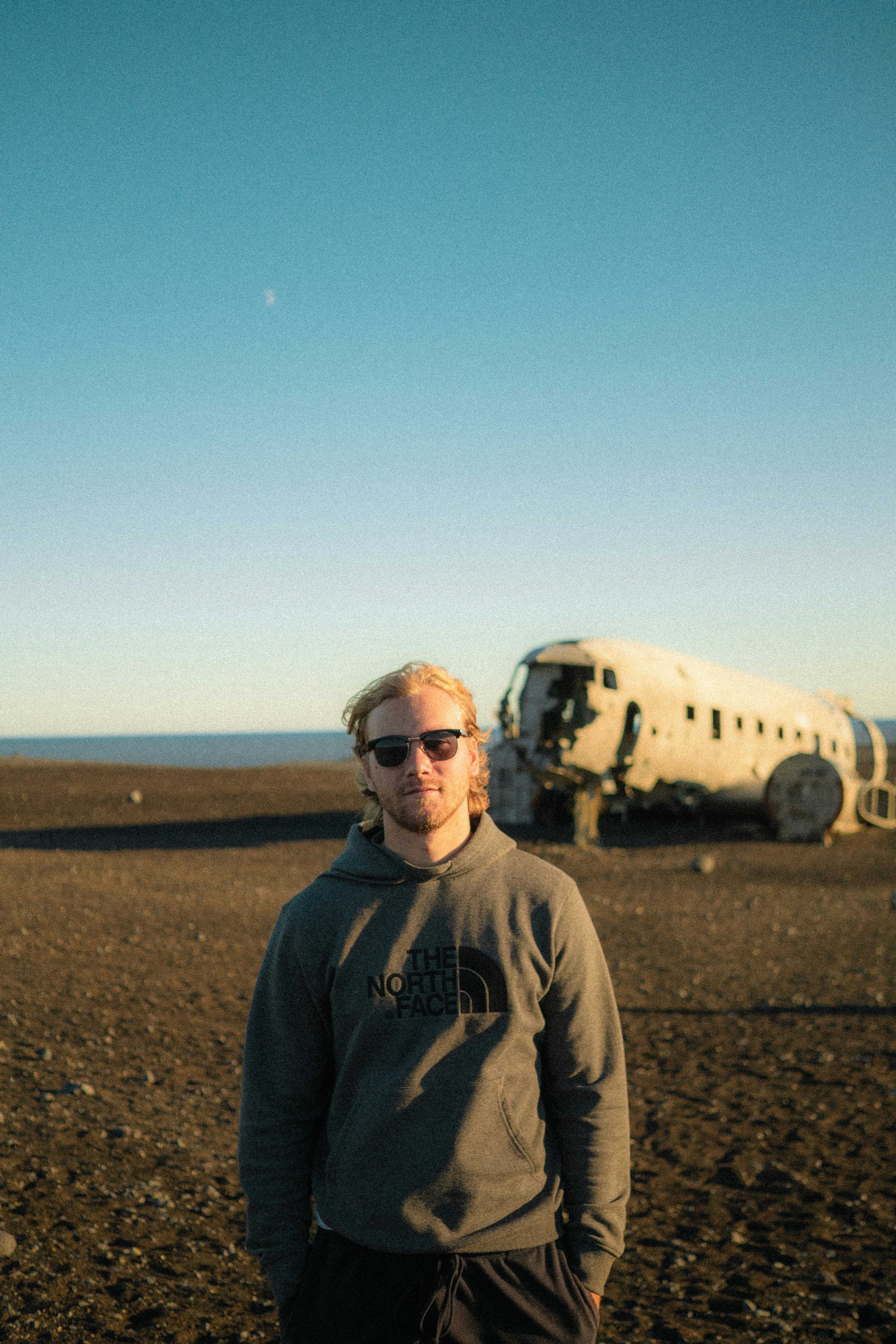 Man in Hoodie Amid Deserted Airframe on a Distant Shore