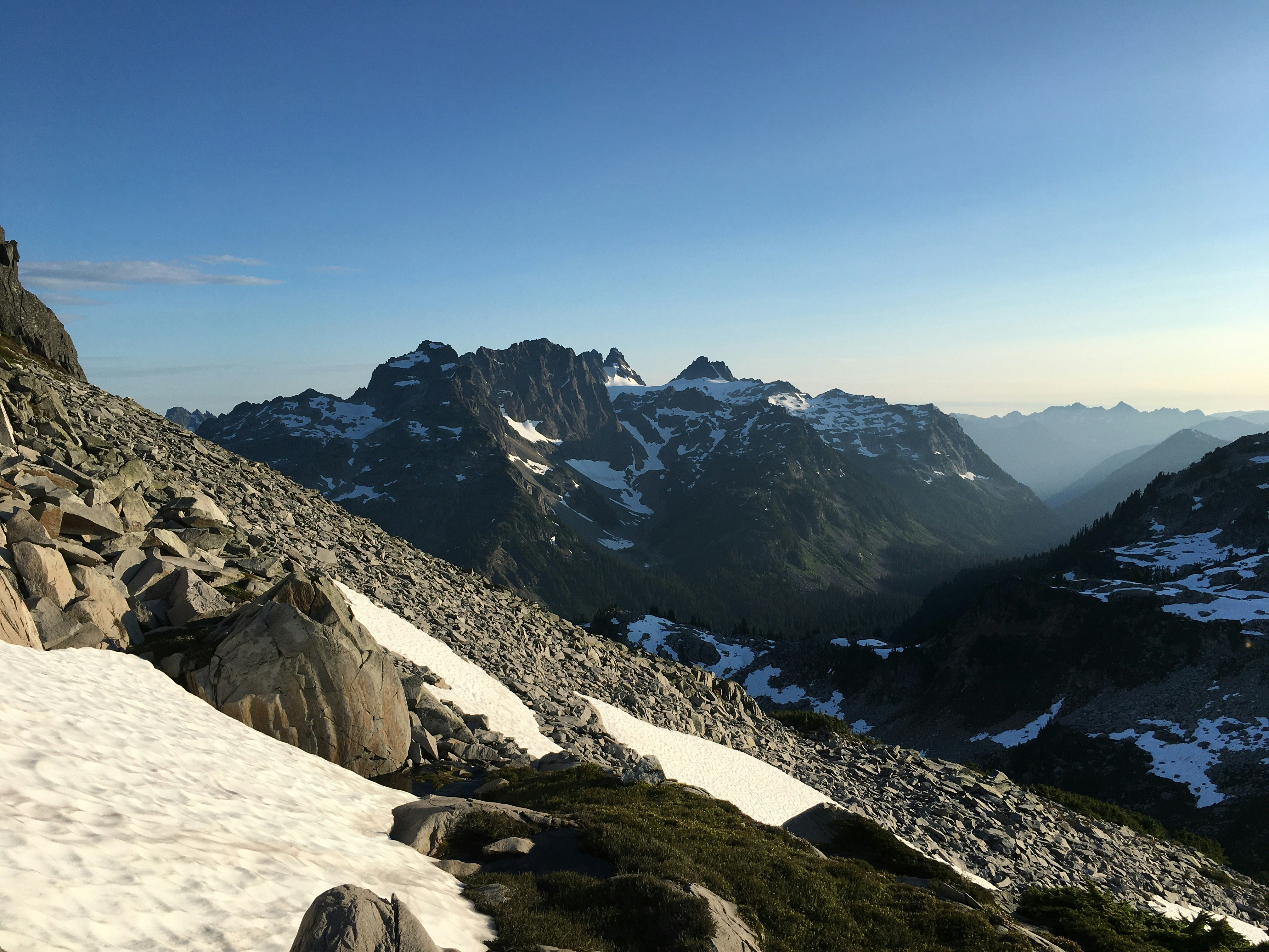 Majestic mountain range with snow-capped peaks and rocky terrain under a clear blue sky. The scene captures the serene beauty of the wilderness.
