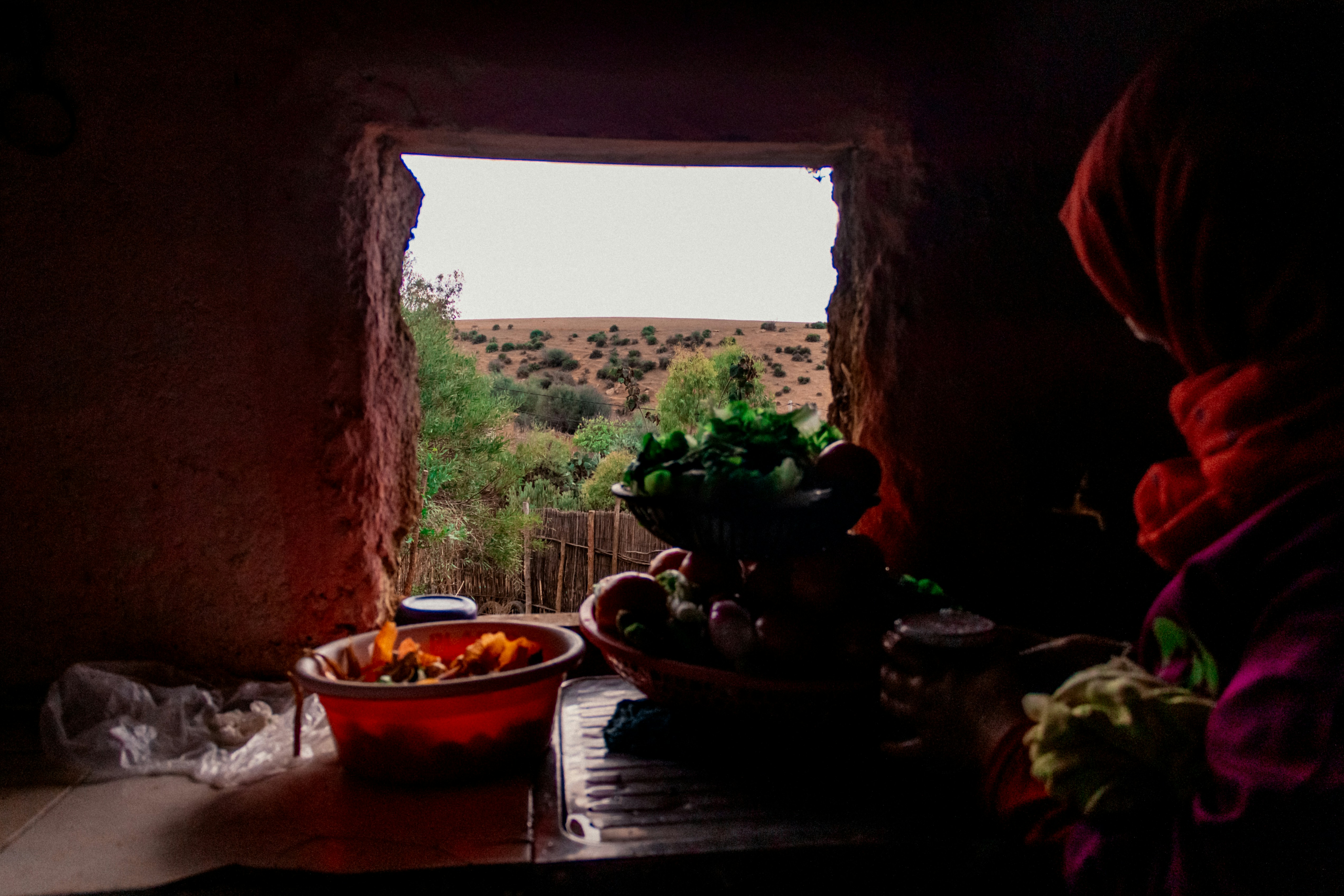 Sunlit doorway and fruit bowl: a dim adobe kitchen scene framed by light