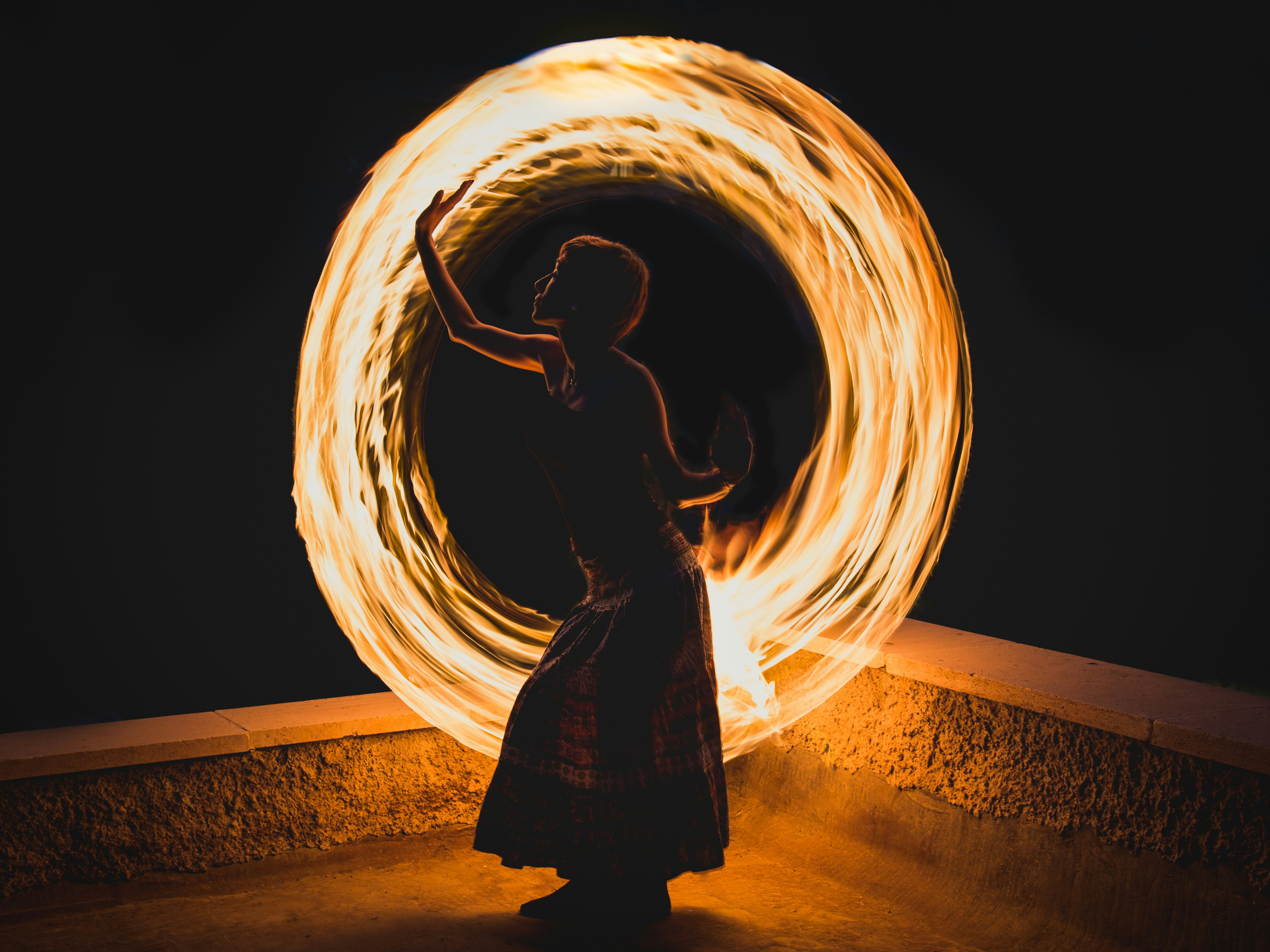Silhouette of a performer spinning fire to create a mesmerizing circular pattern against a dark backdrop.